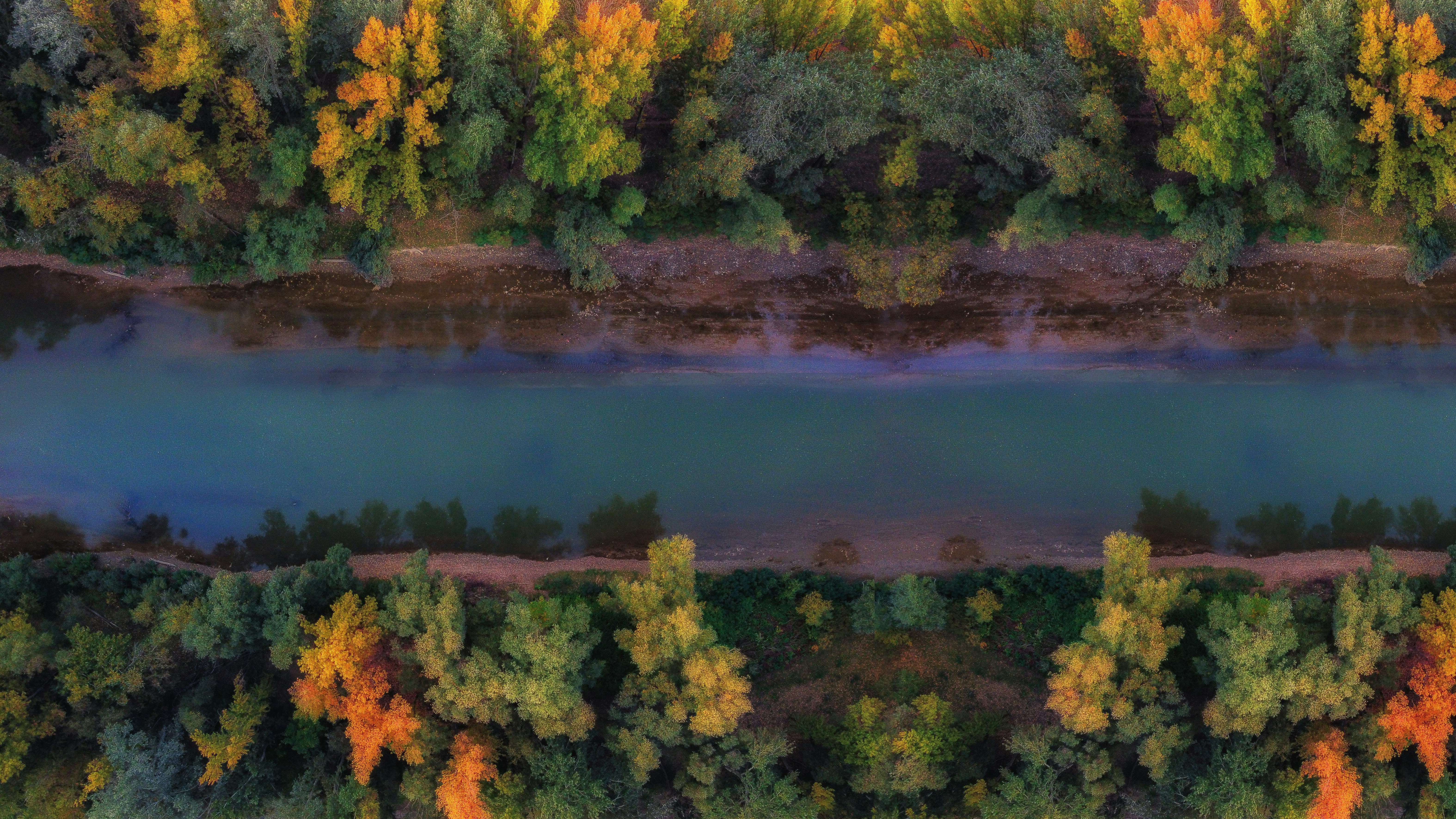 Aerial view of a river flanked by vibrant autumn foliage, creating a symmetrical landscape.