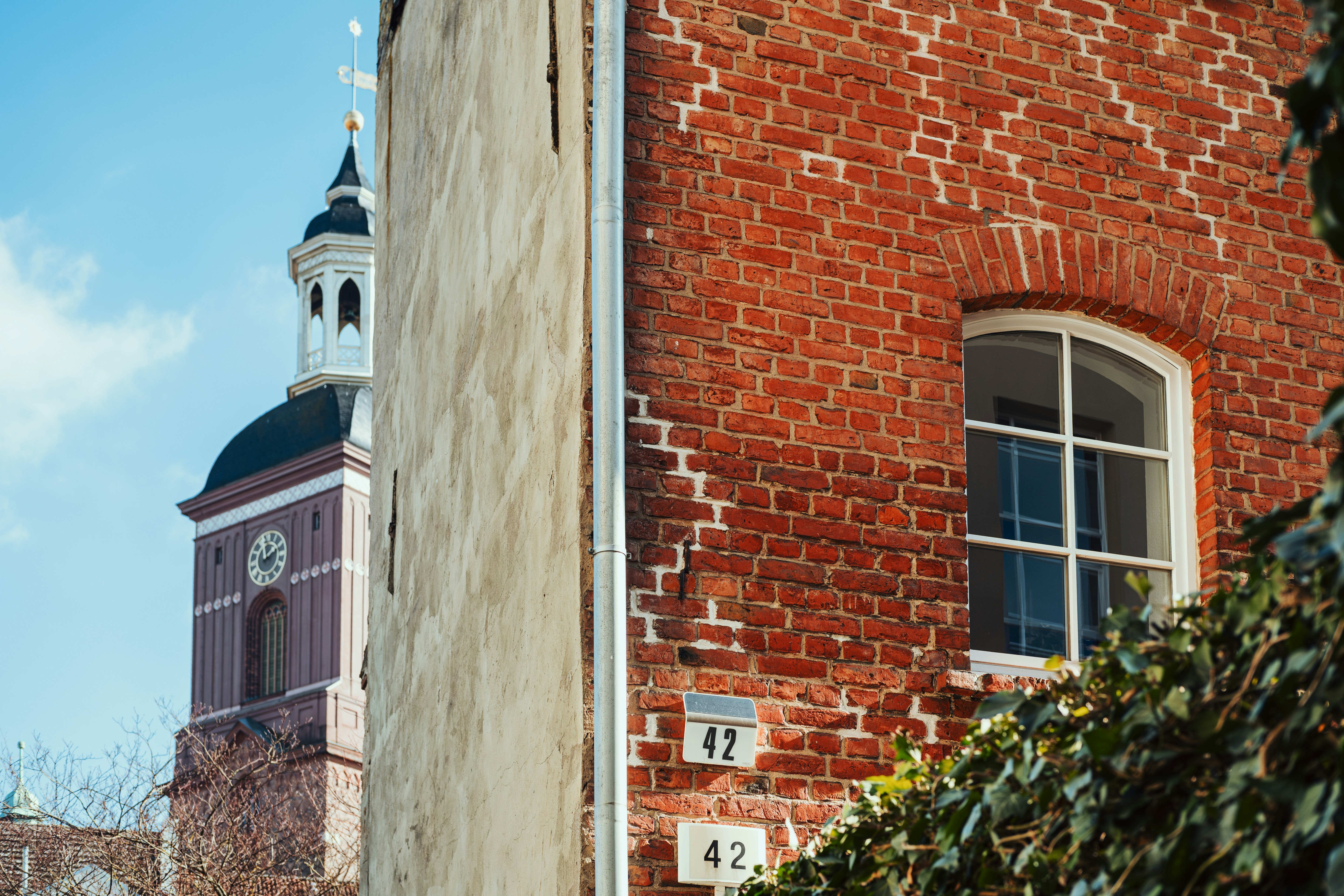 Red brick building with arched window beside a clock tower against a clear blue sky.