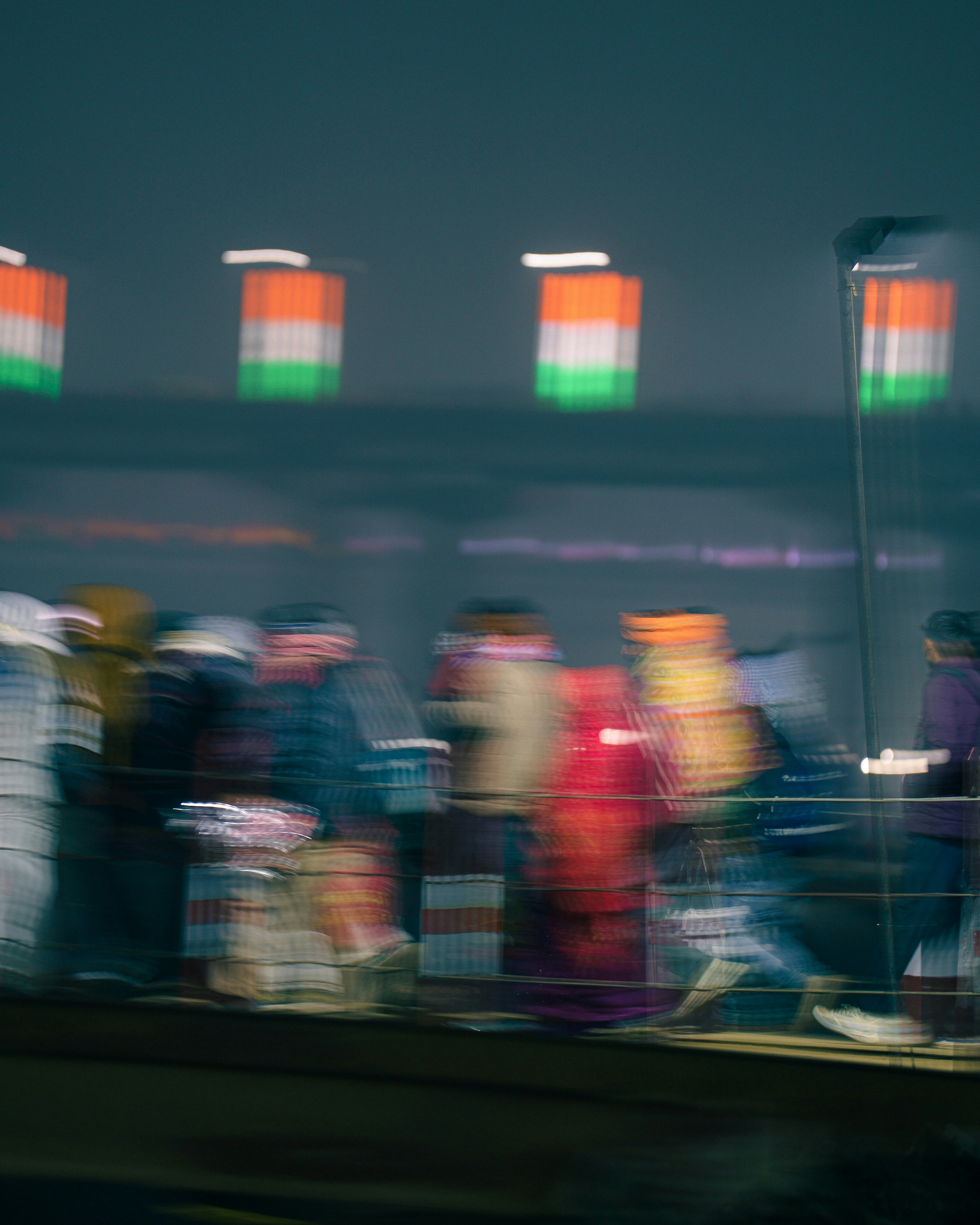 Blurred figures of a crowd moving under illuminated flags, showcasing the vibrant energy of a festive gathering at night.