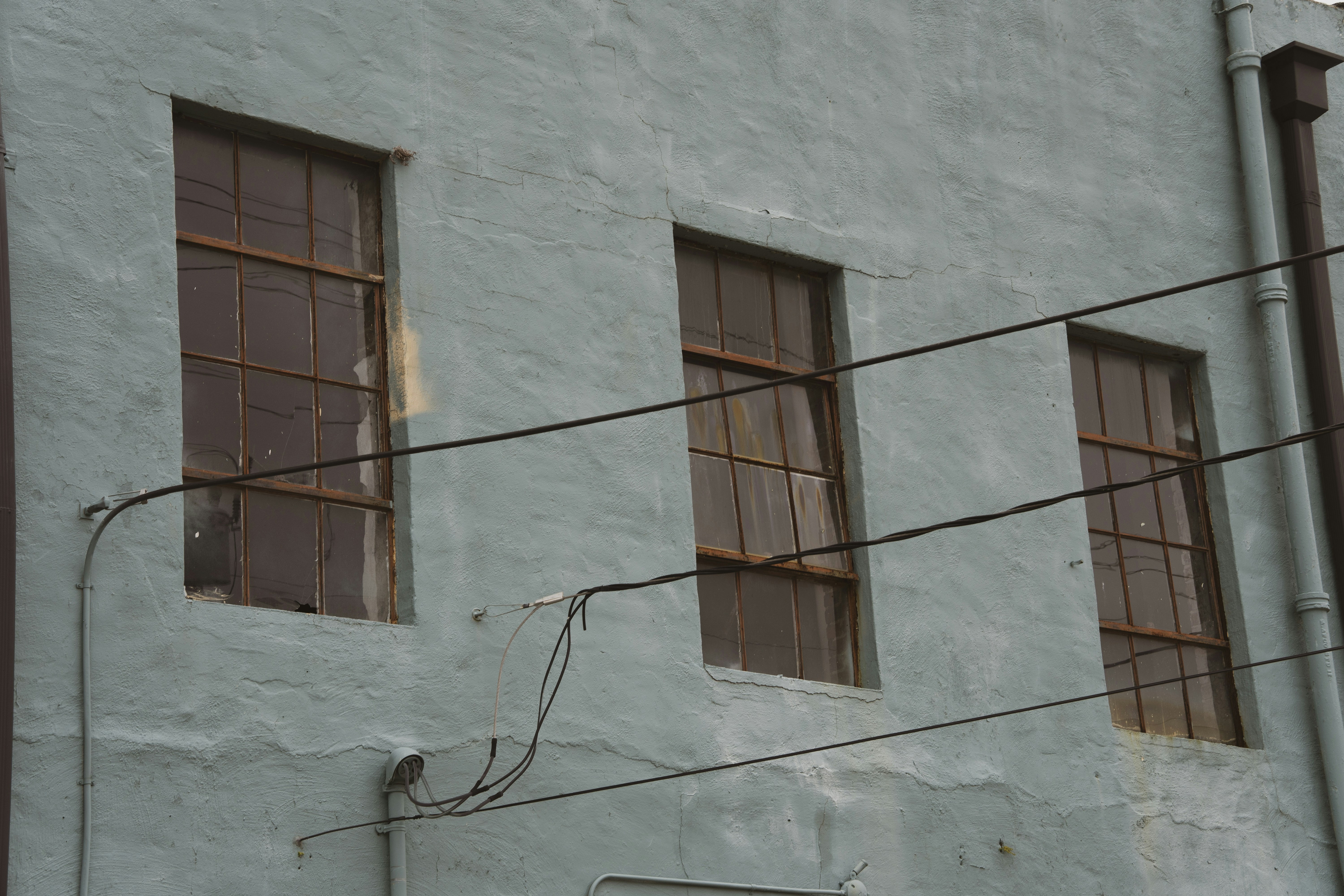 Three Windows on a Teal Facade, Strung by Wires: An Urban Minimalist Study