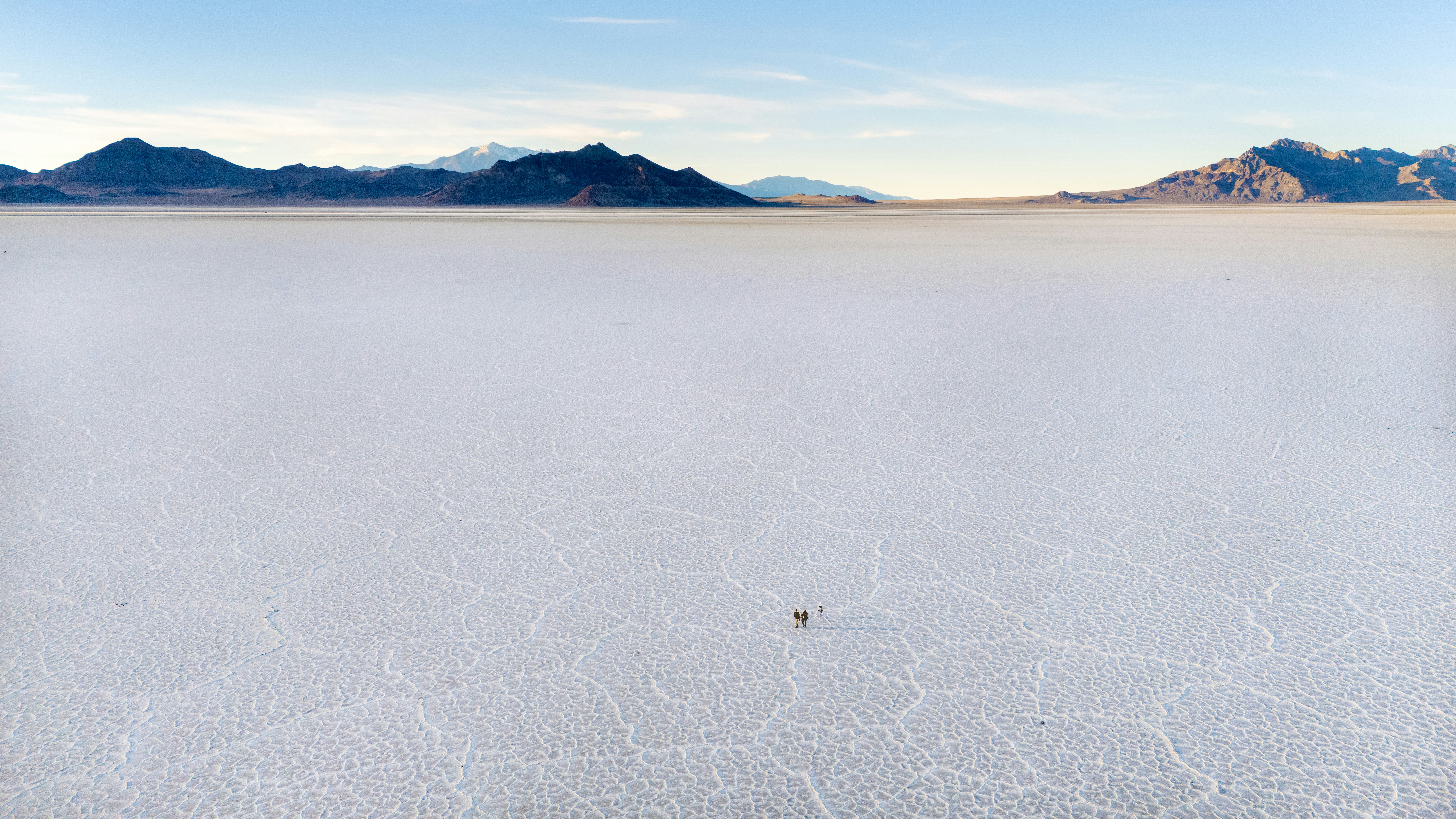 Family walking across expansive salt flats with distant mountains under a clear blue sky.