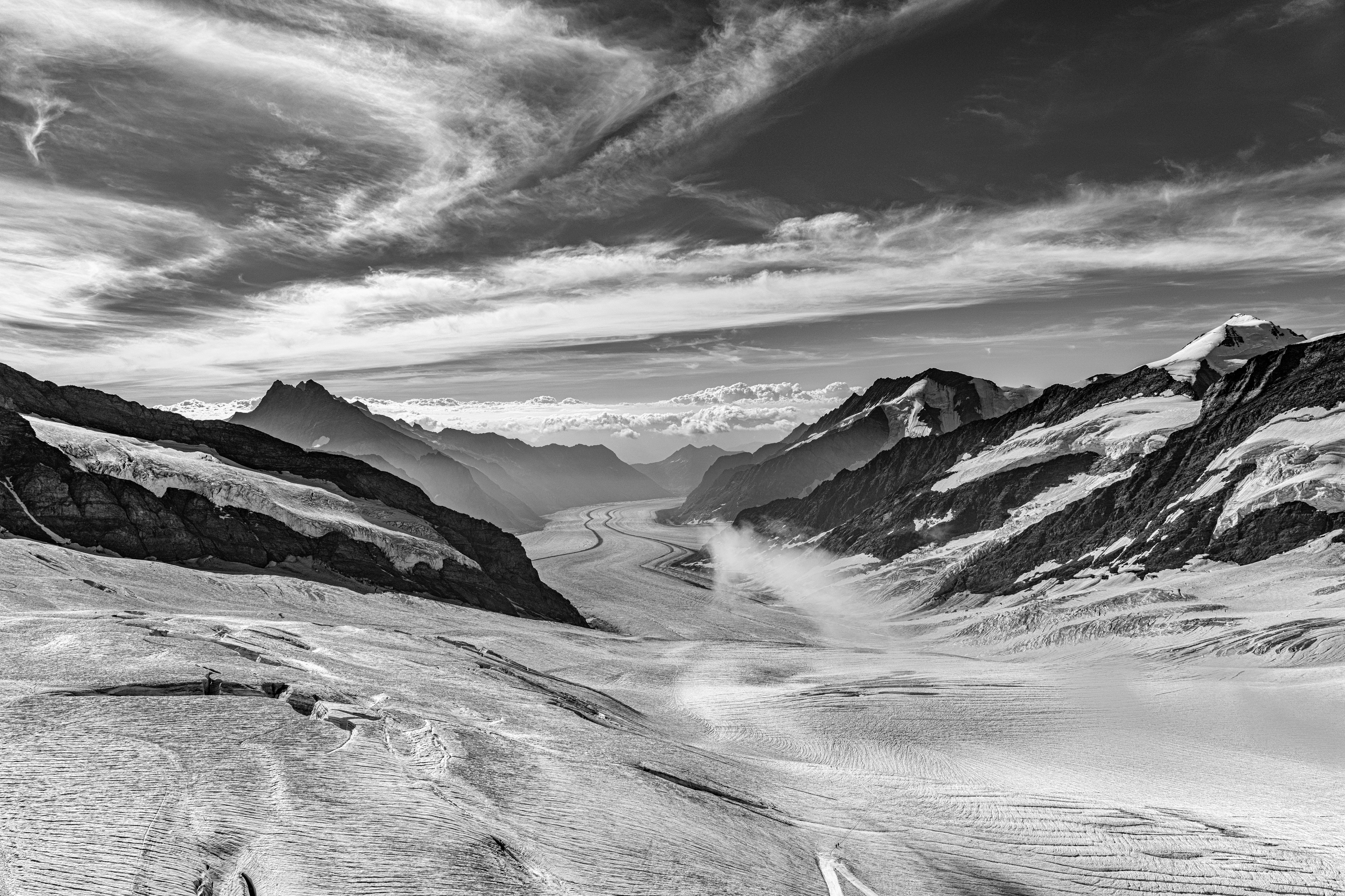Sweeping view of a glacier winding through rugged mountain terrain under a dramatic sky.