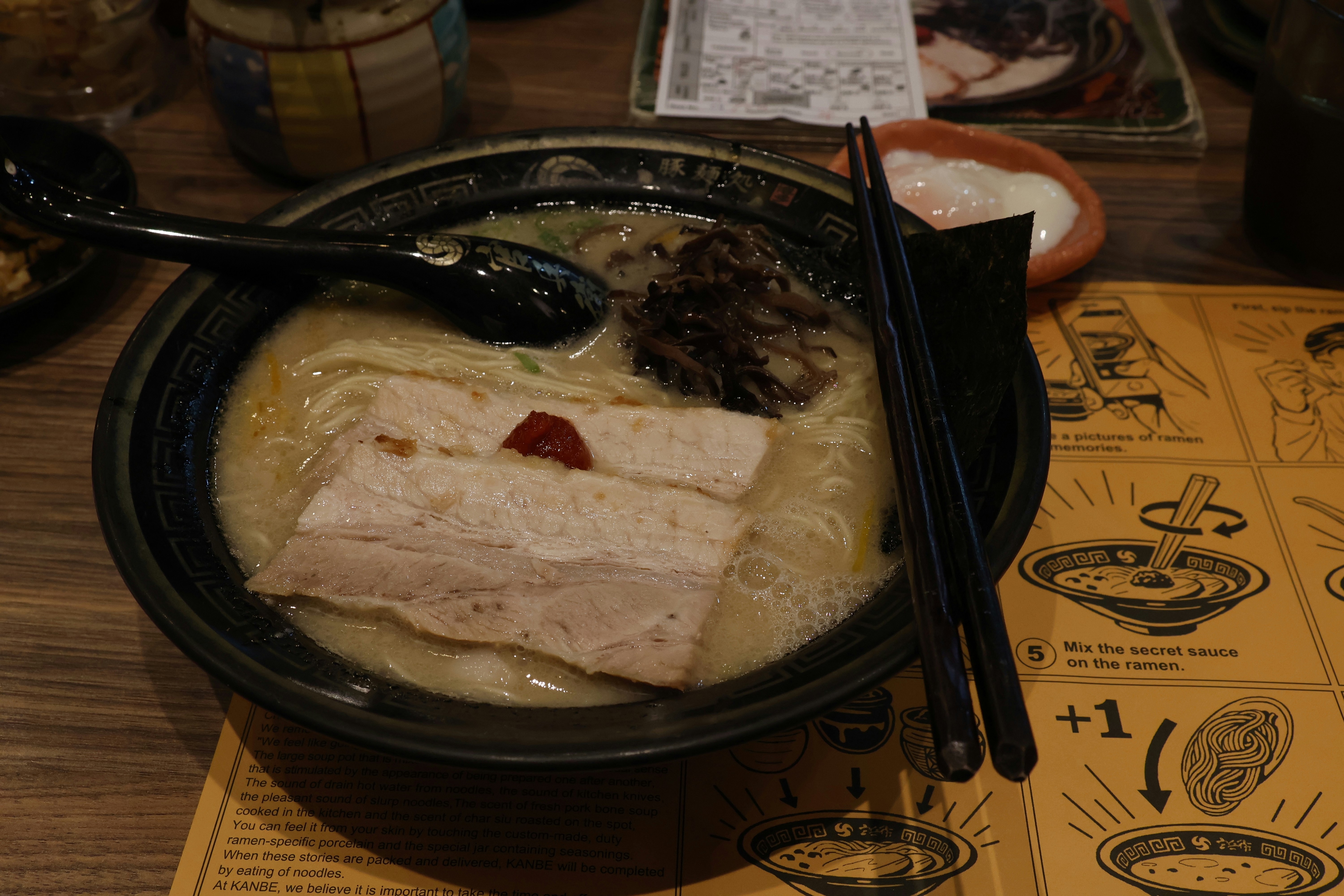 Bowl of ramen with sliced pork, a red garnish, and seaweed on a wooden table.