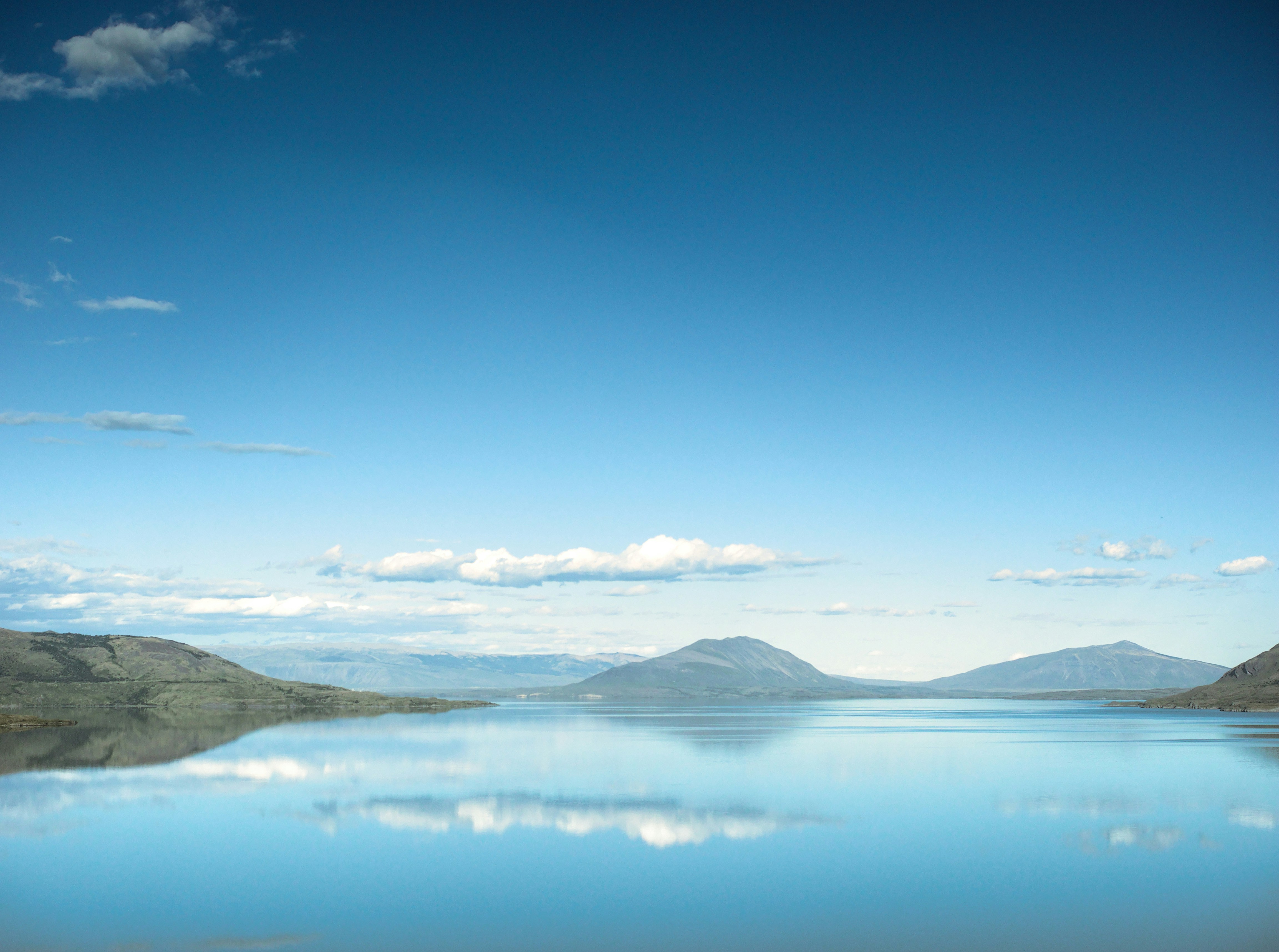 Calm lake mirroring distant mountains under a clear blue sky.