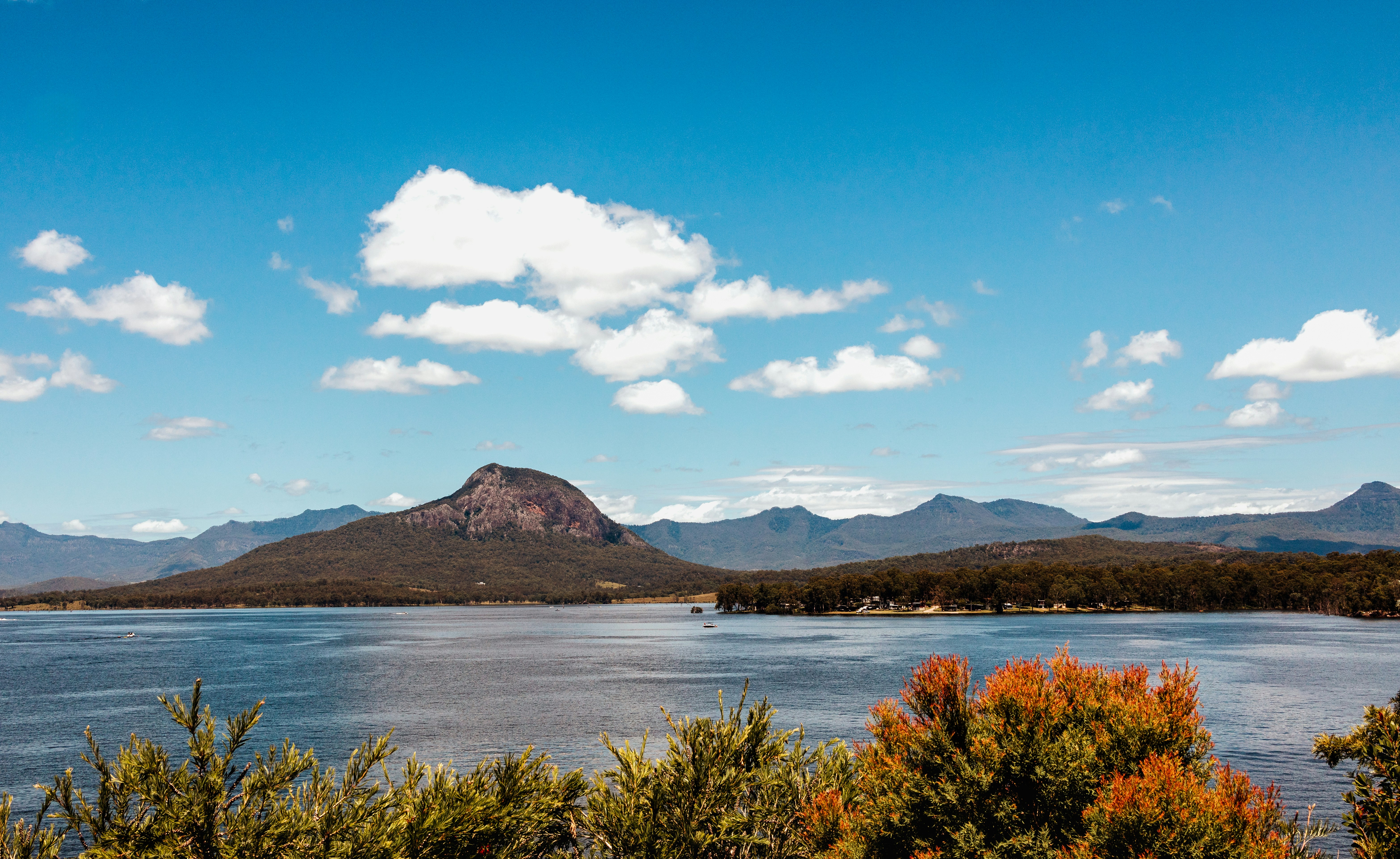 Mountain range under a vibrant blue sky with scattered clouds overlooking a tranquil lake.
