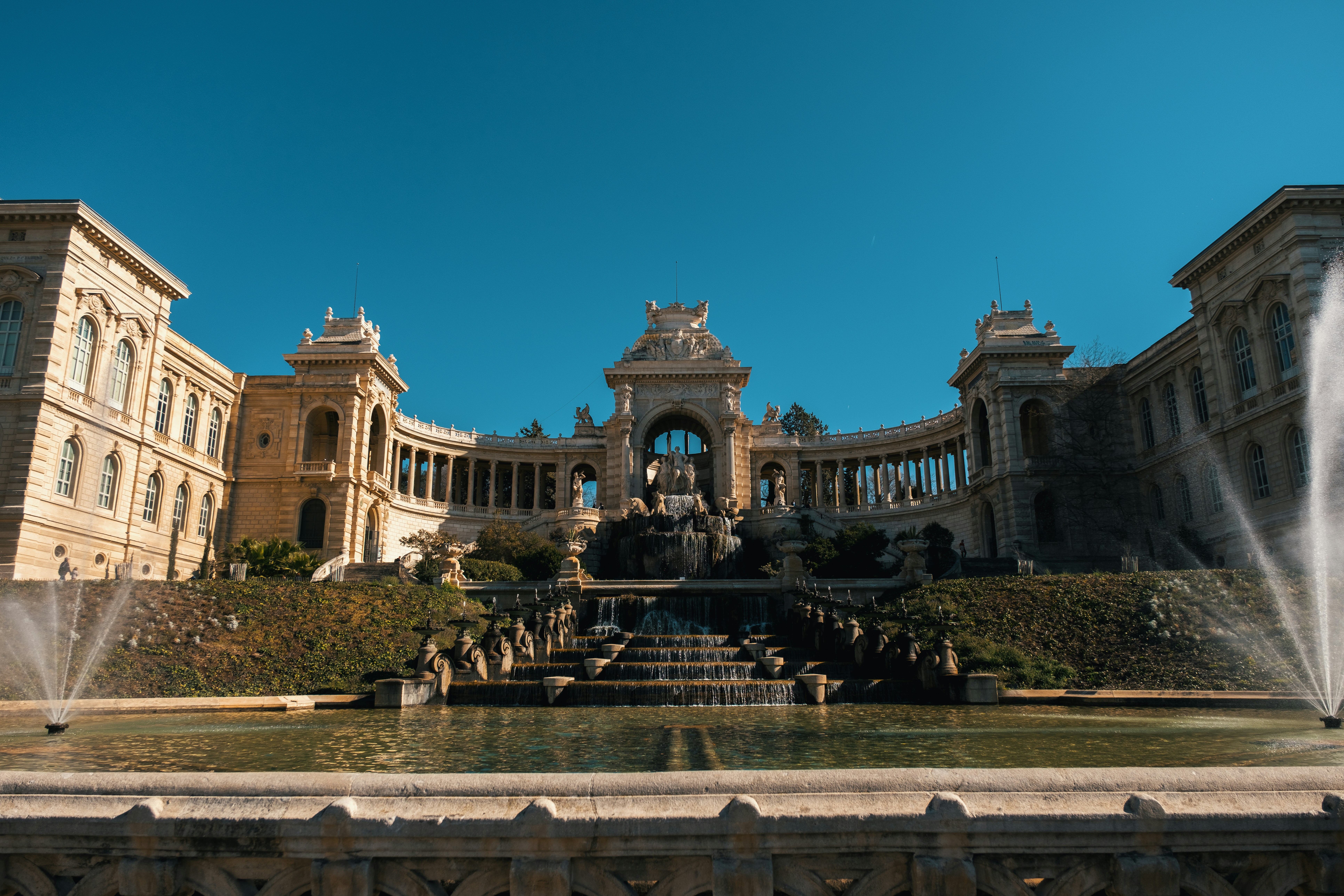 Grand neoclassical building with cascading fountain and clear blue sky.