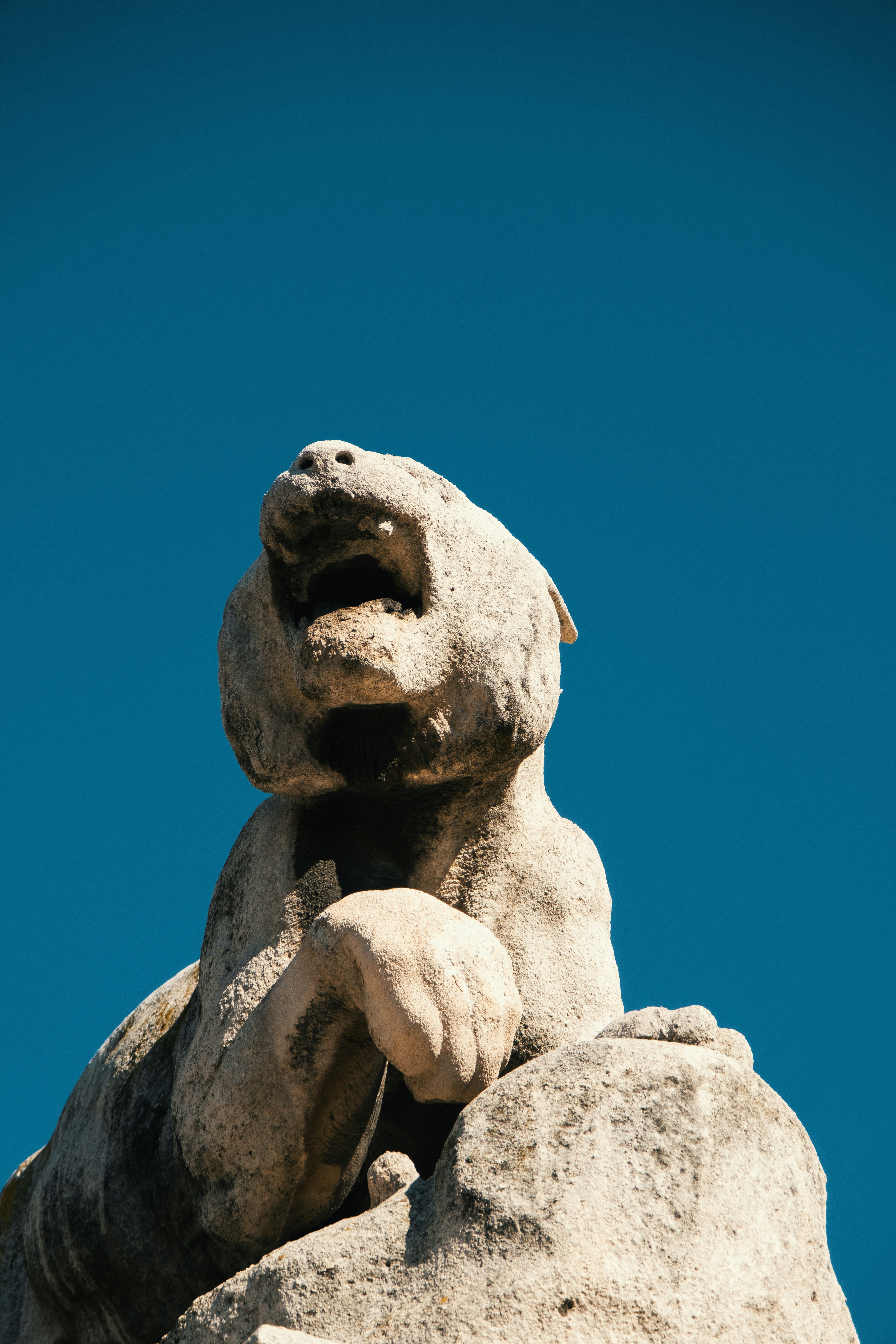 Weathered Sentinel: Stone Dog Perched Against a Cobalt Sky