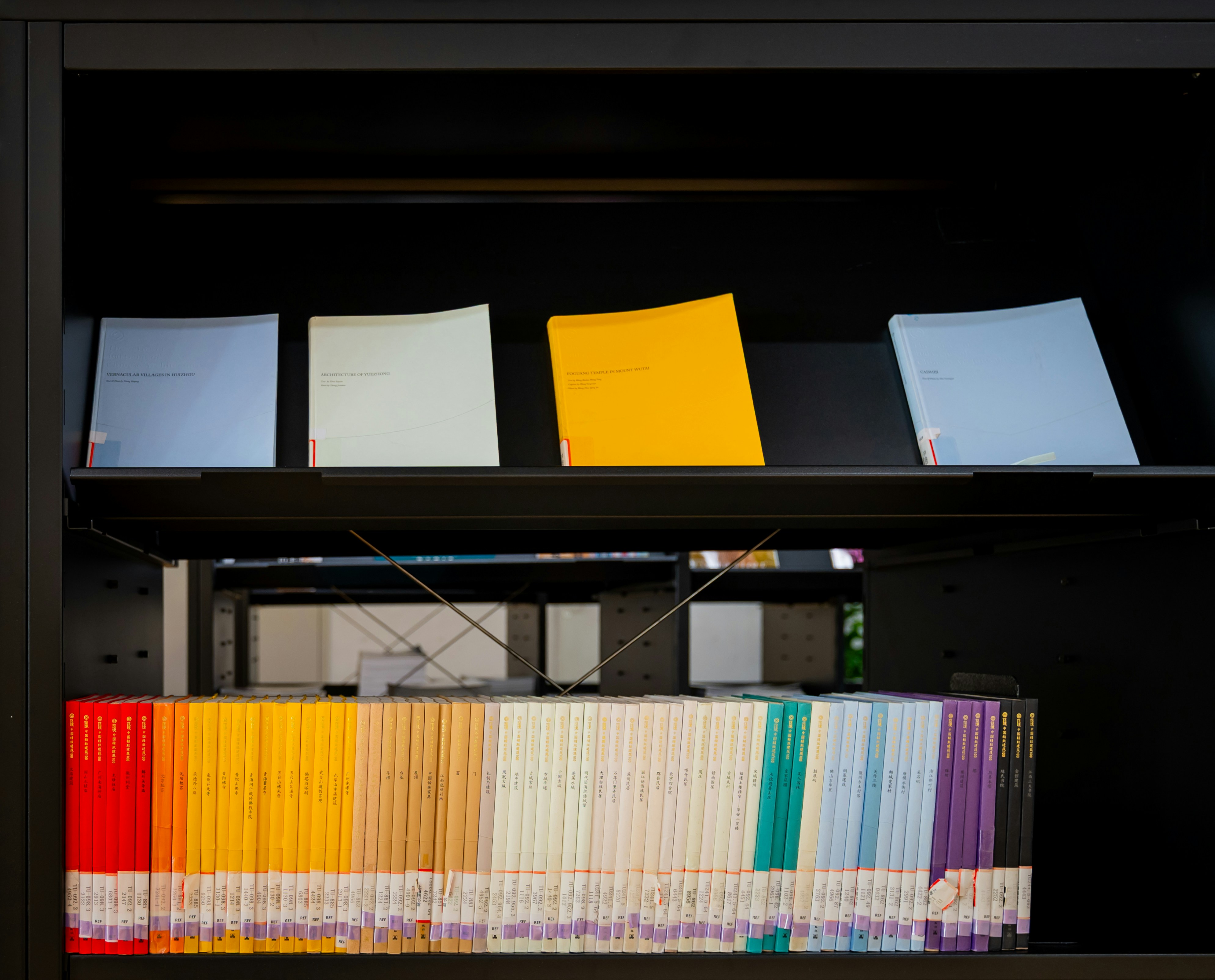 Colorful books arranged neatly on a black shelf, creating a gradient from reds to blues.