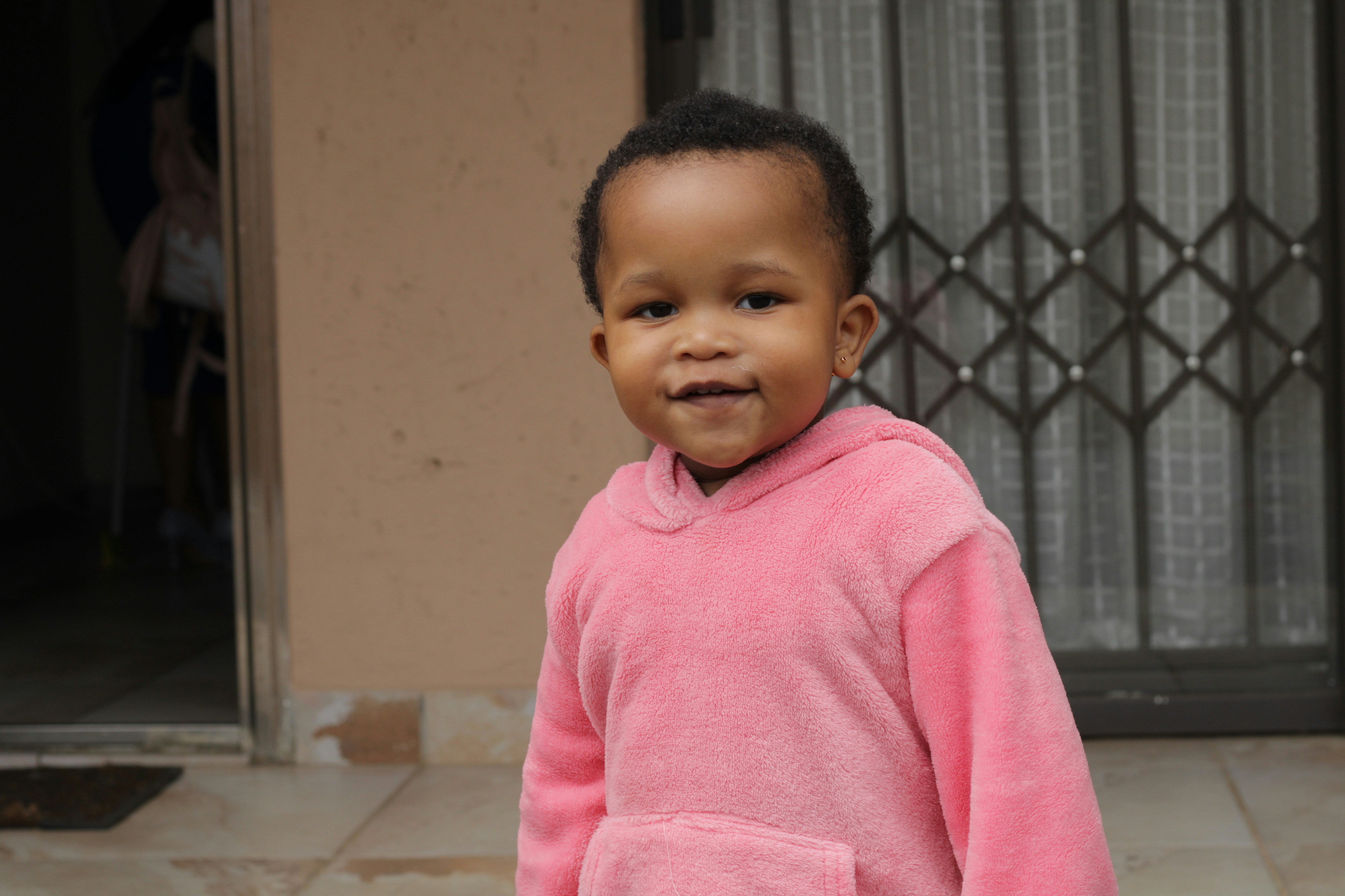 Child in a pink hoodie standing outdoors with a gentle smile.