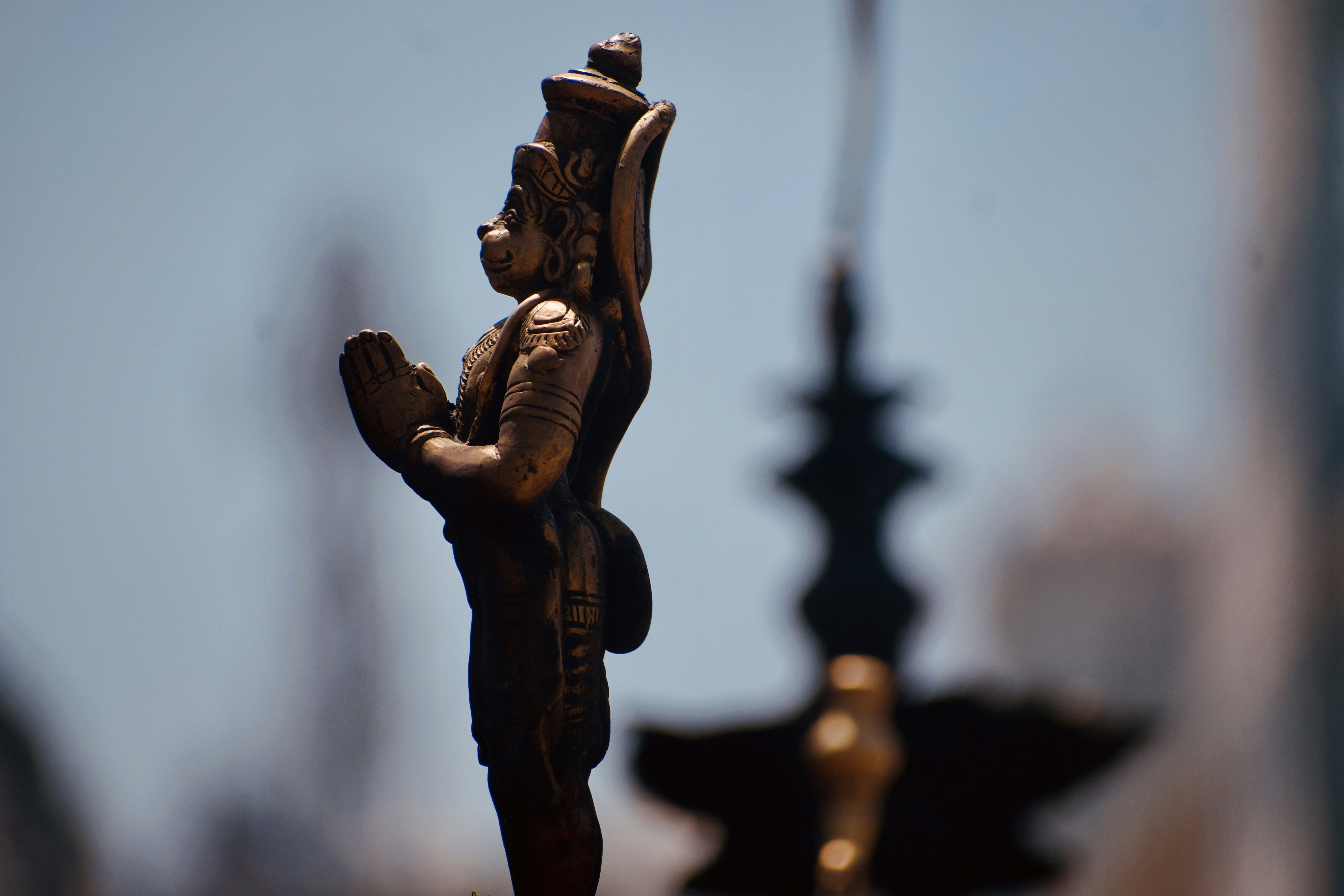 Bronze statue of a deity in prayer against a blurred background with muted colors.