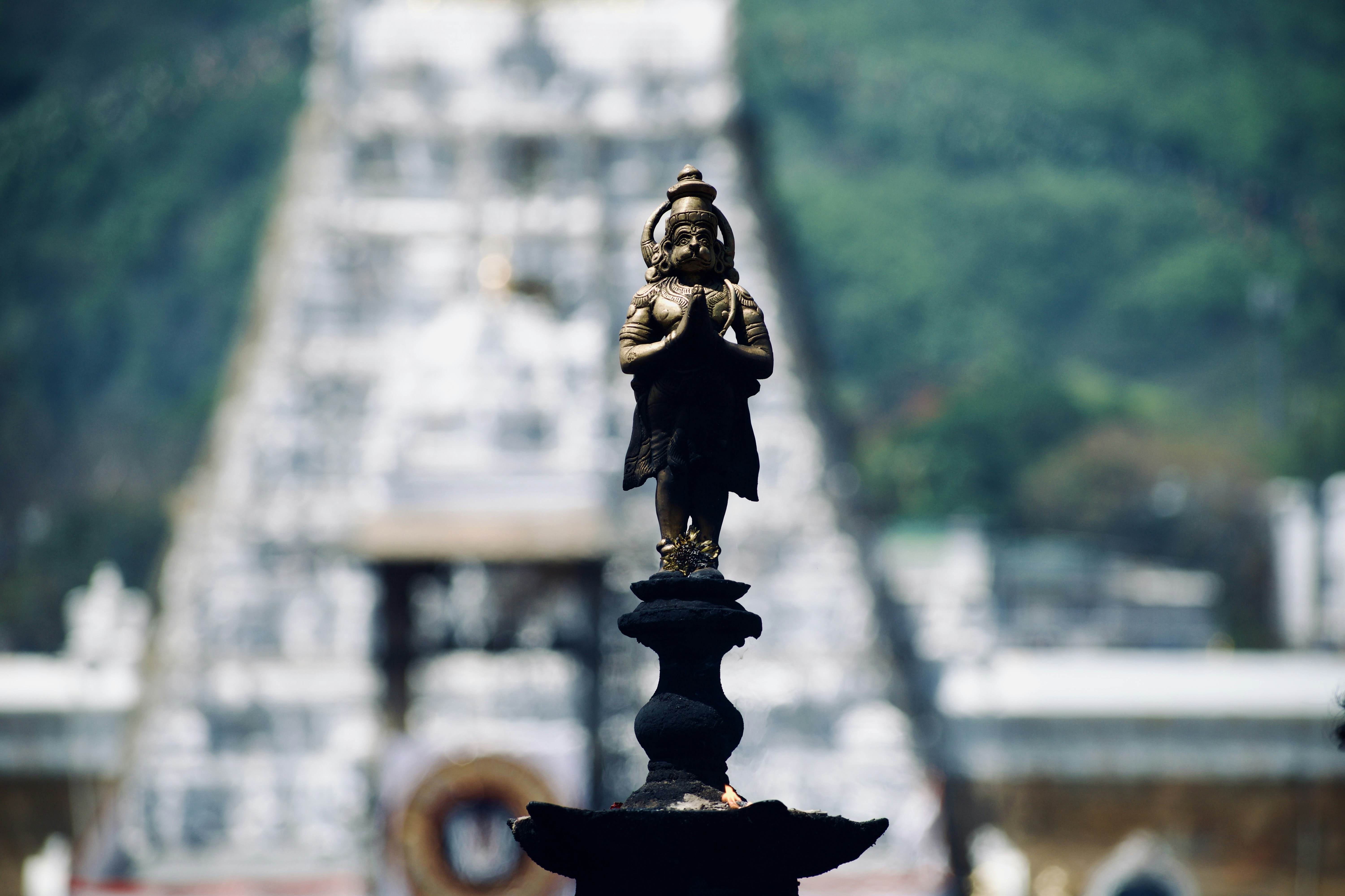 Bronze statue in prayer posture with temple facade blurred in the background.