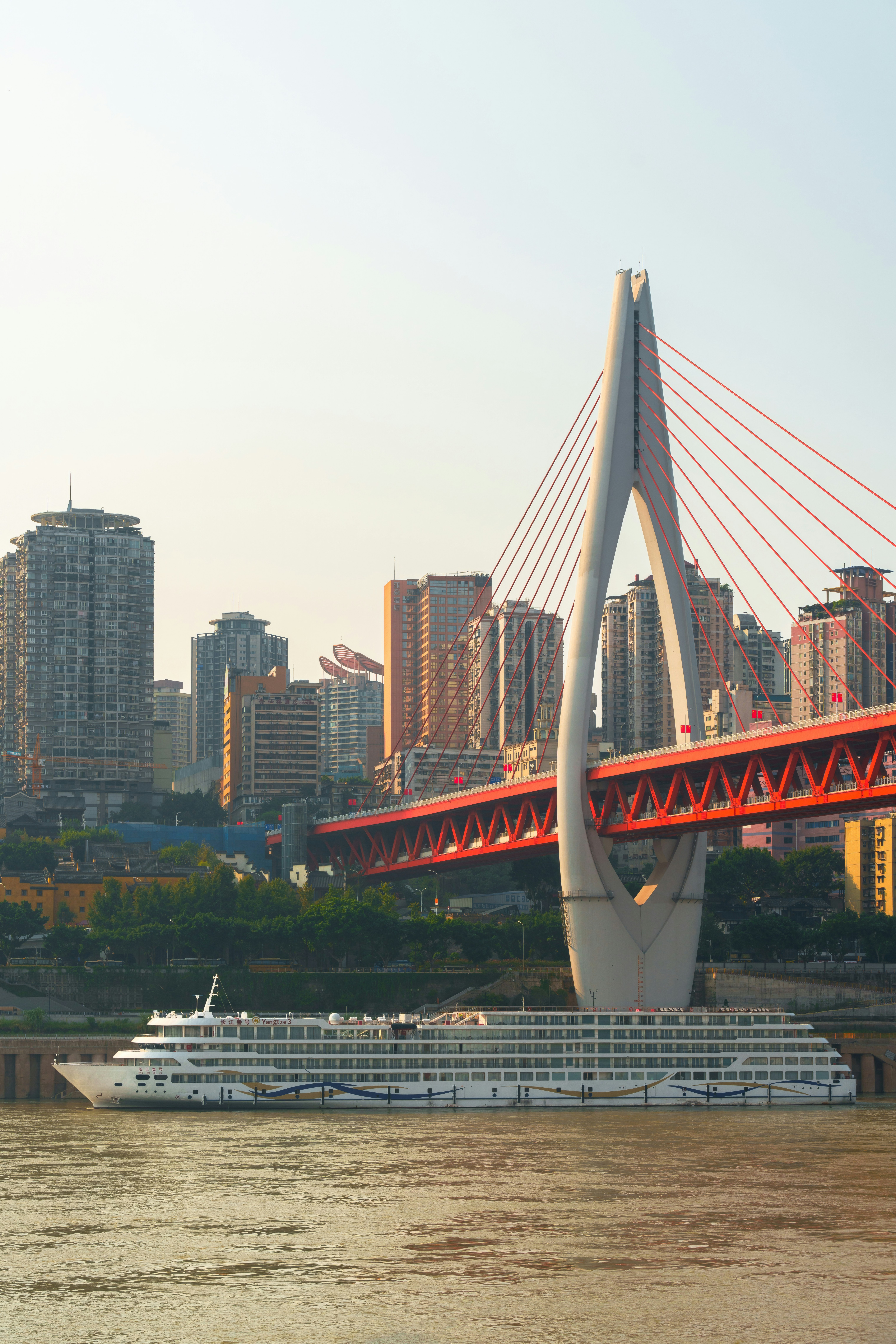 Crimson Cables Over the River: Bridge Framing a Riverside Cruise