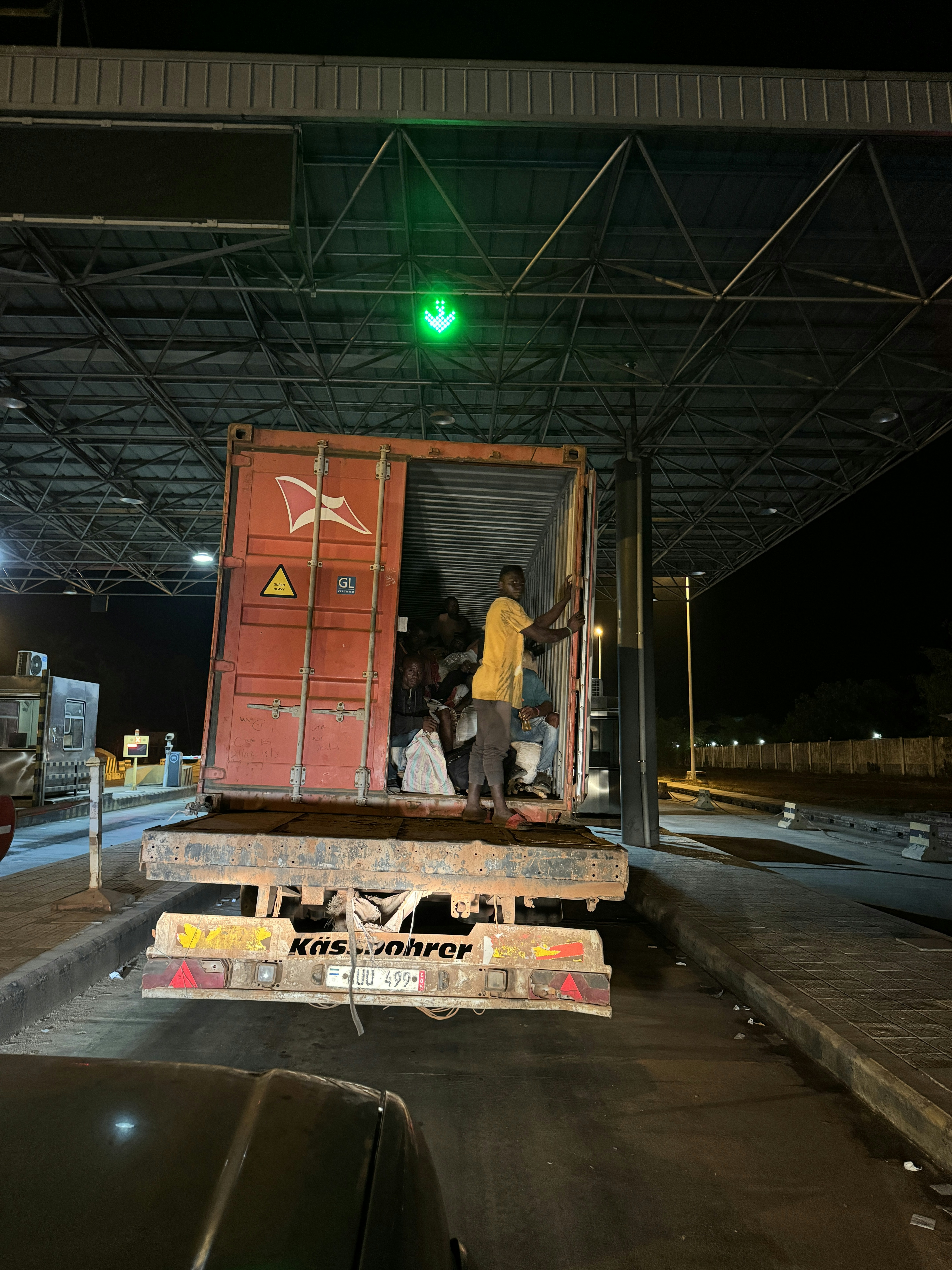 Truck driver managing cargo at a toll booth under nighttime lighting.