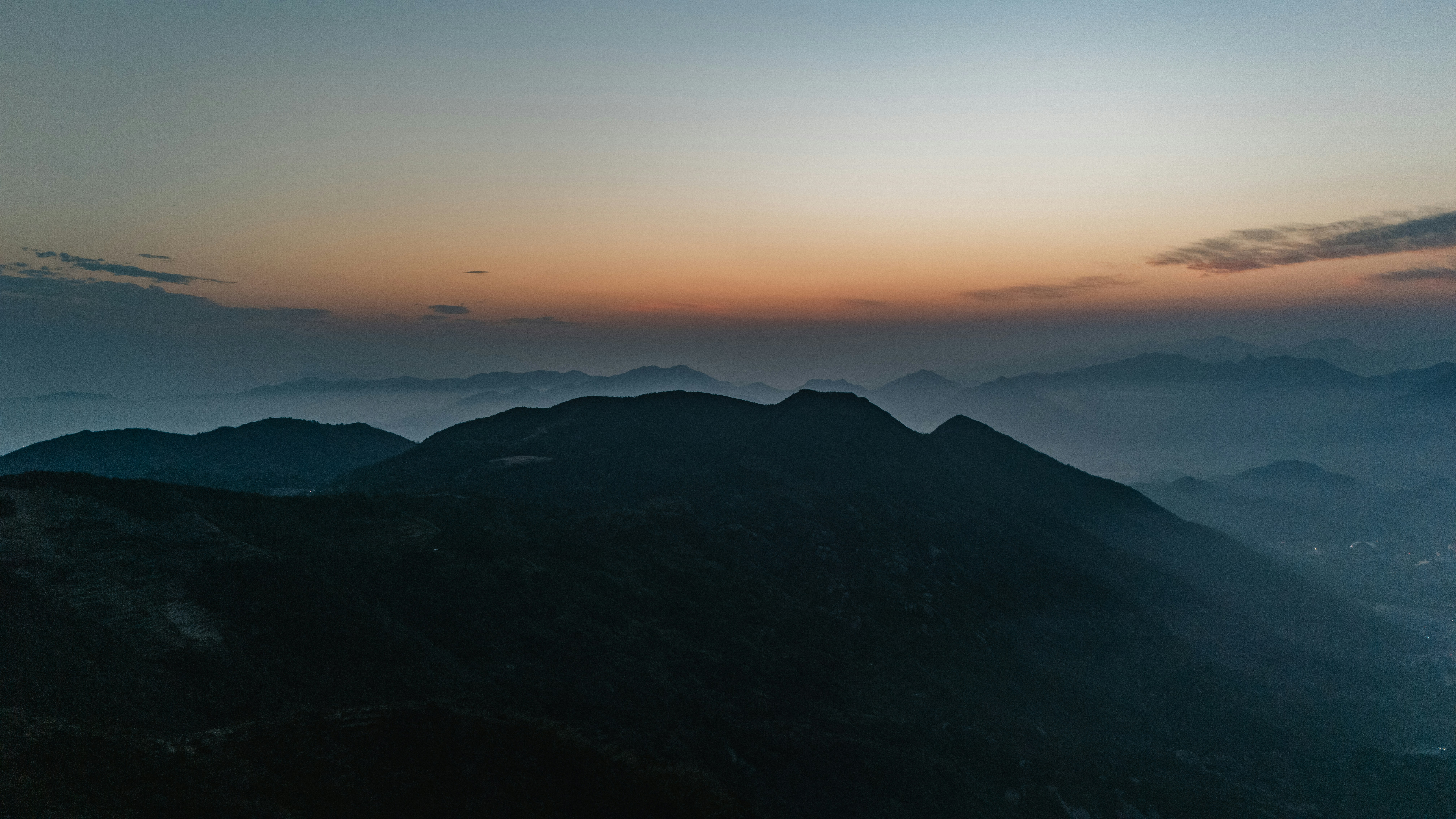 Silhouetted mountains under a tranquil twilight sky with soft gradients of orange and blue.
