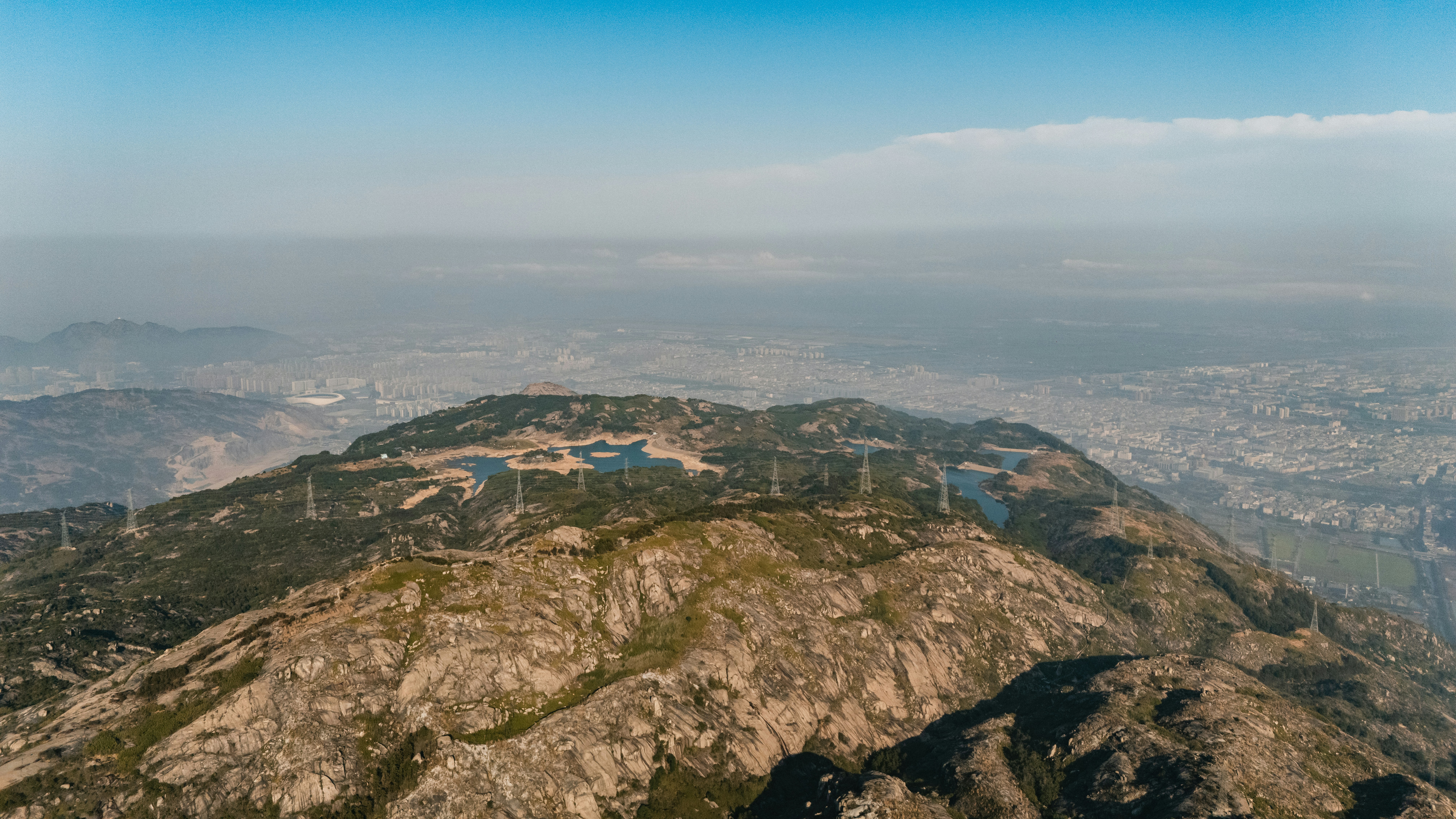 Rocky mountain terrain with scattered lakes overlooking a sprawling city under a blue sky.