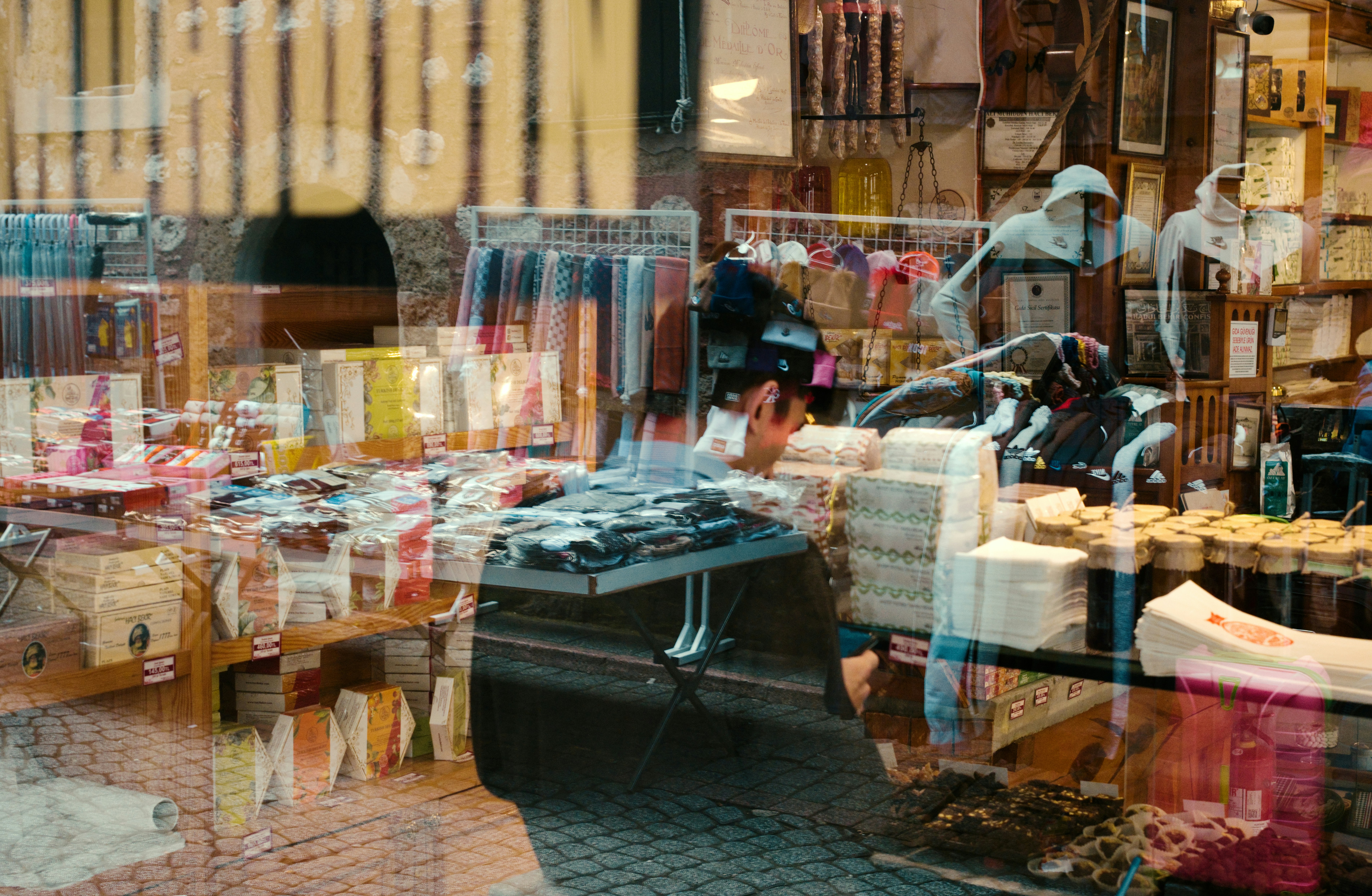 Complex reflection of a bustling market stall on a glass window, merging indoor and outdoor elements.
