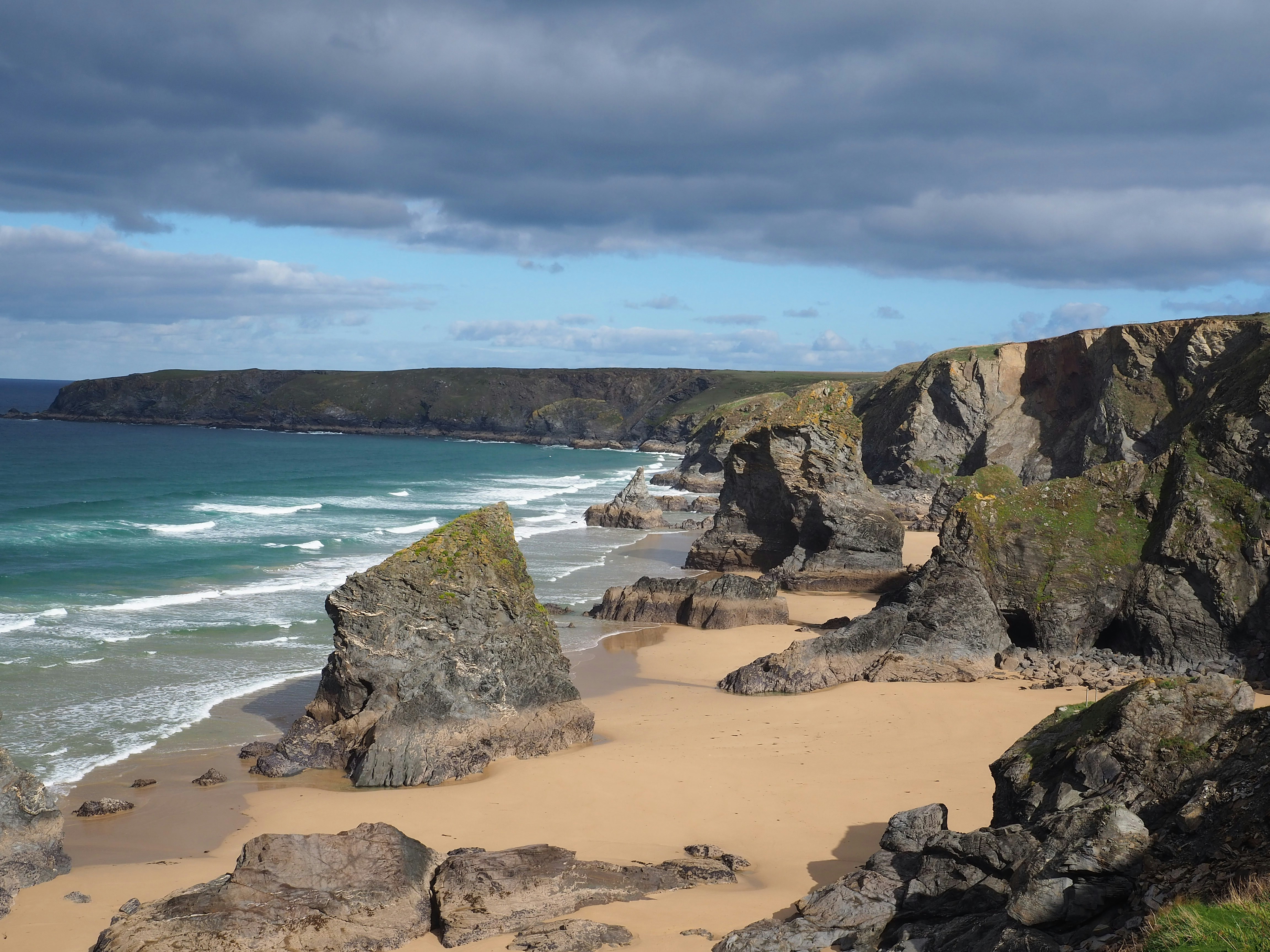 Rocky cliffs and sandy beach with waves under a partly cloudy sky.
