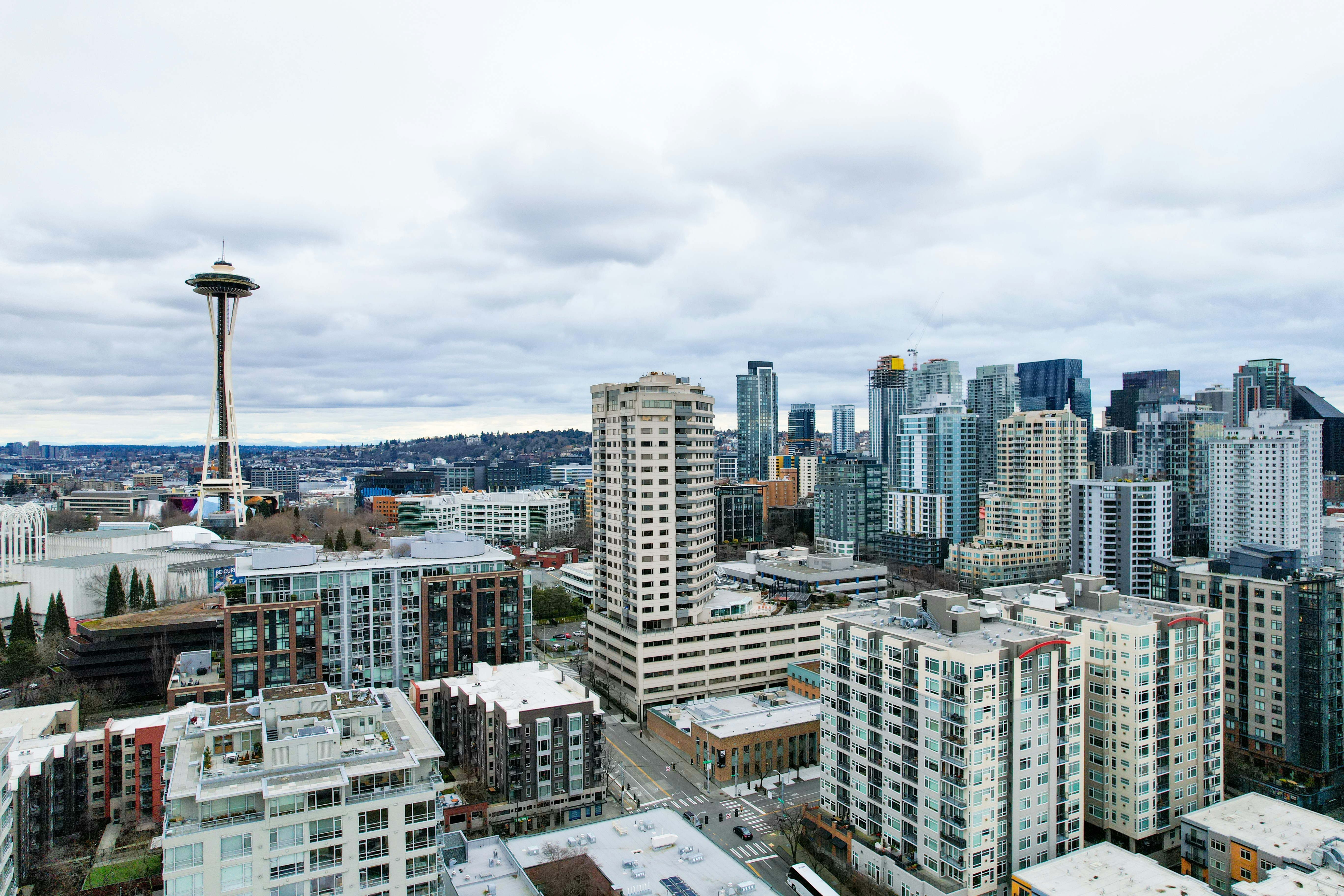 Seattle skyline with the Space Needle towering over modern high-rises under a cloudy sky.