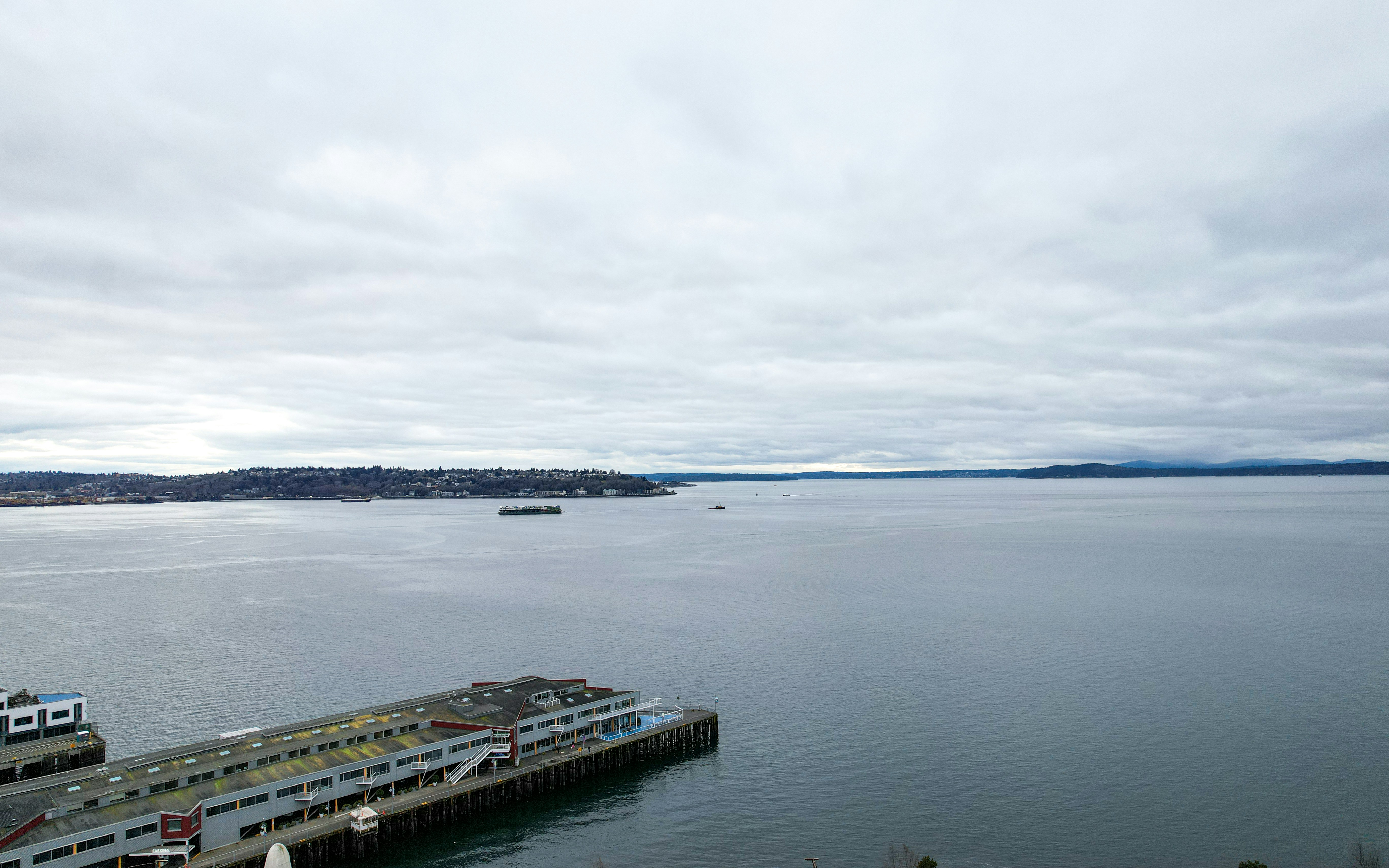 Expansive view of the Seattle waterfront with a ferry crossing the calm waters under a cloudy sky.