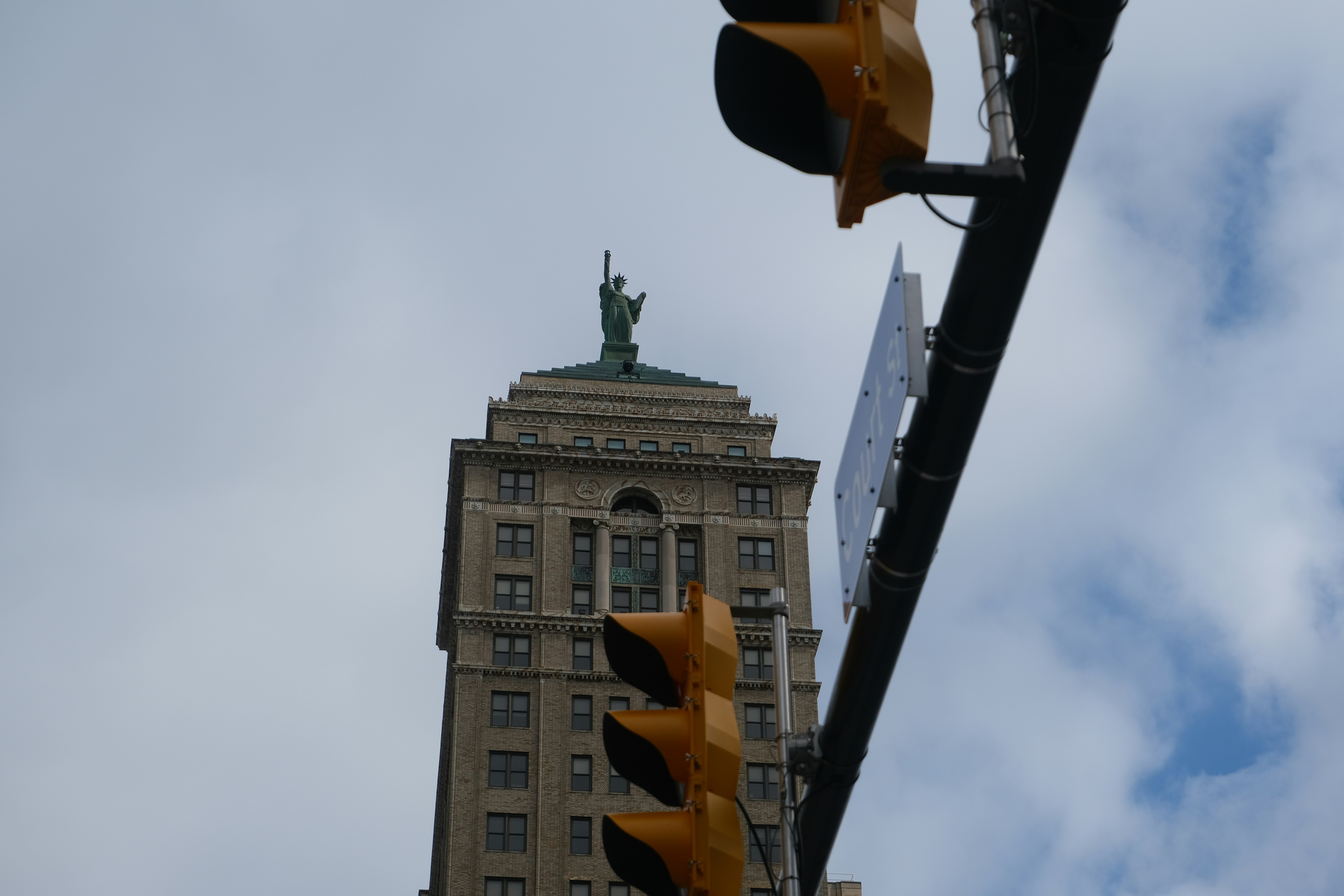 Statue-topped building behind a traffic light under a cloudy sky.