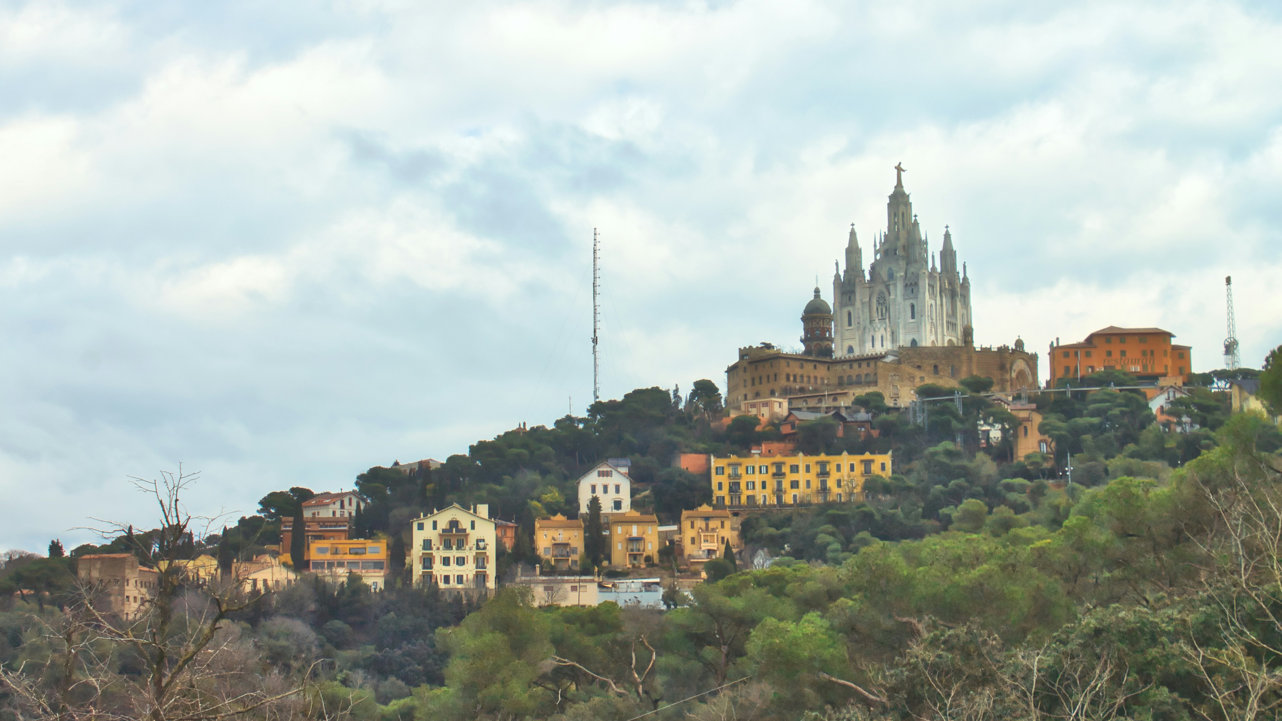 Historic church towers over vibrant hillside village under a cloudy sky.