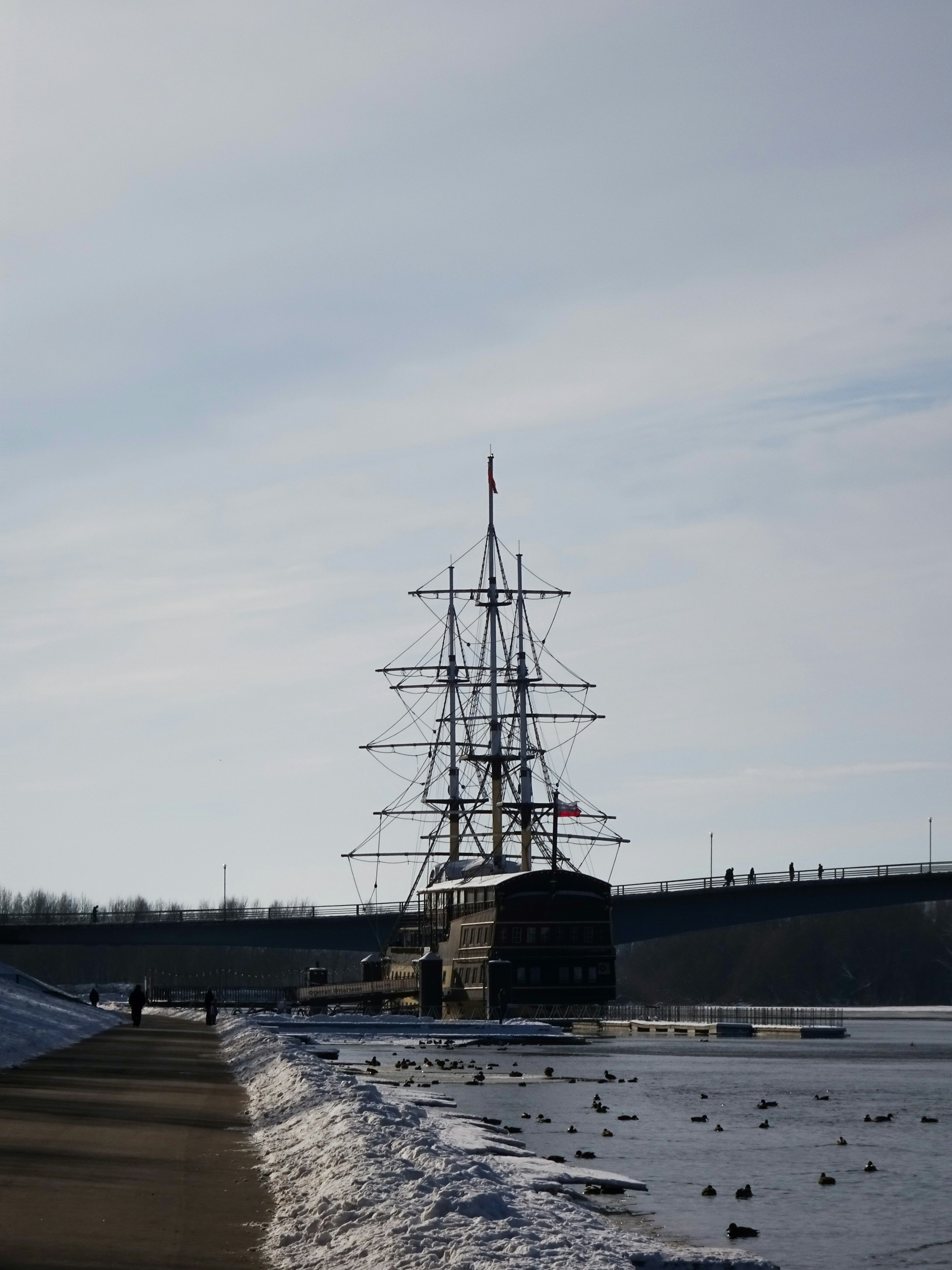 Tall ship docked along a snowy shoreline under a cloudy sky.