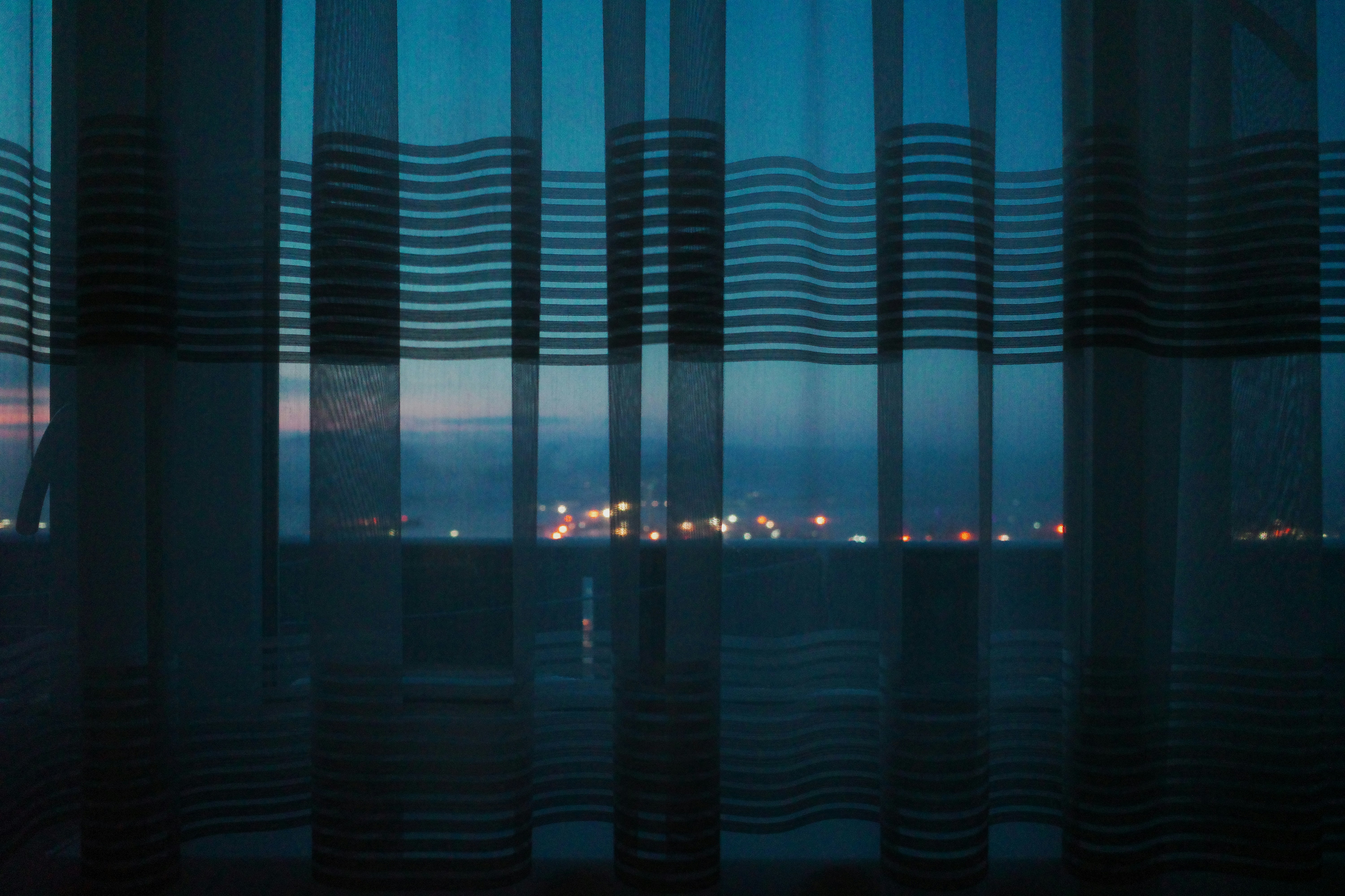 City lights softly glow through sheer curtains at dusk.