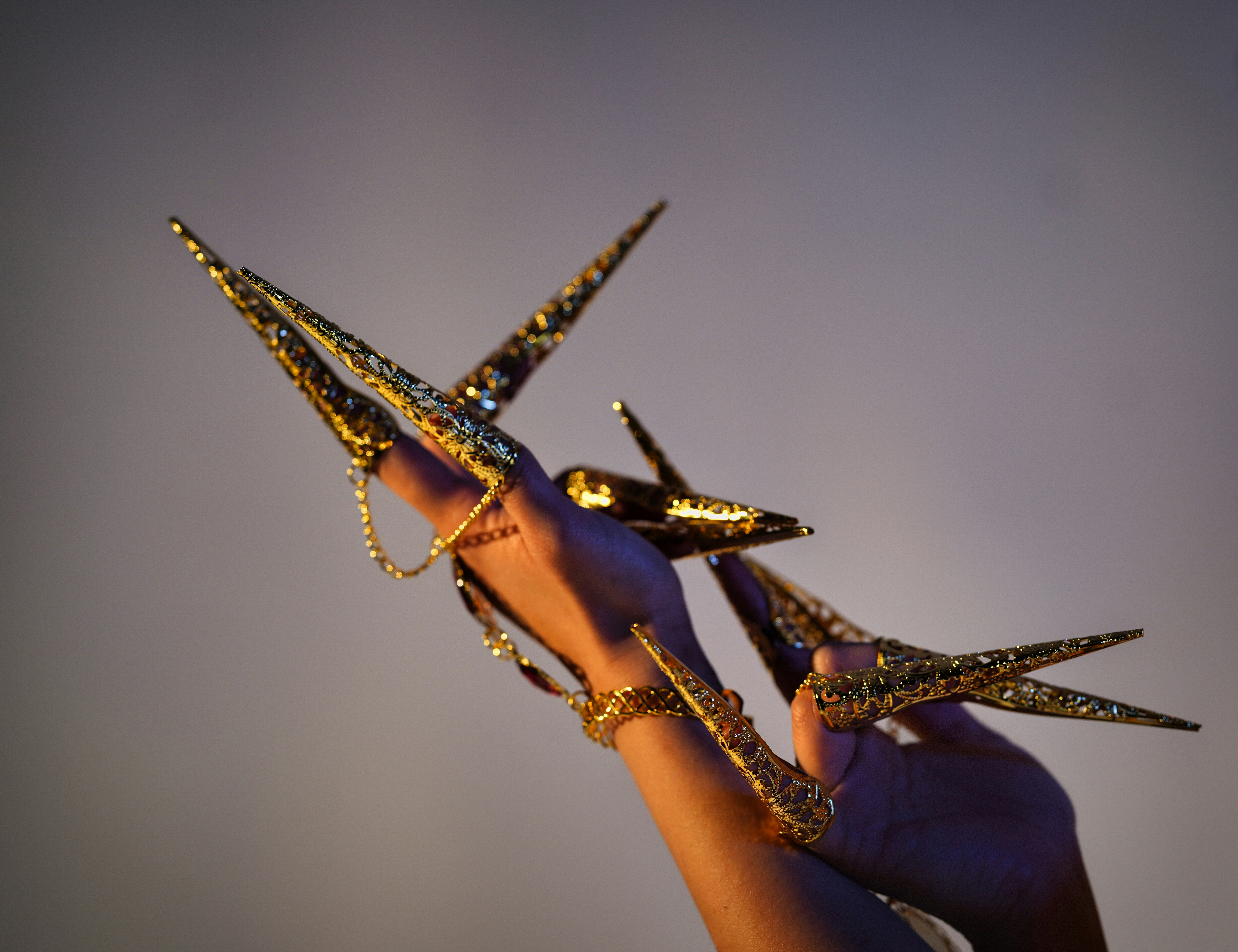 Elongated golden claws extend from delicate hands, shimmering with intricate details against a muted background. A fusion of elegance and power, this image captures the essence of adornment as both beauty and armor—a bold statement of style and craftsmanship.