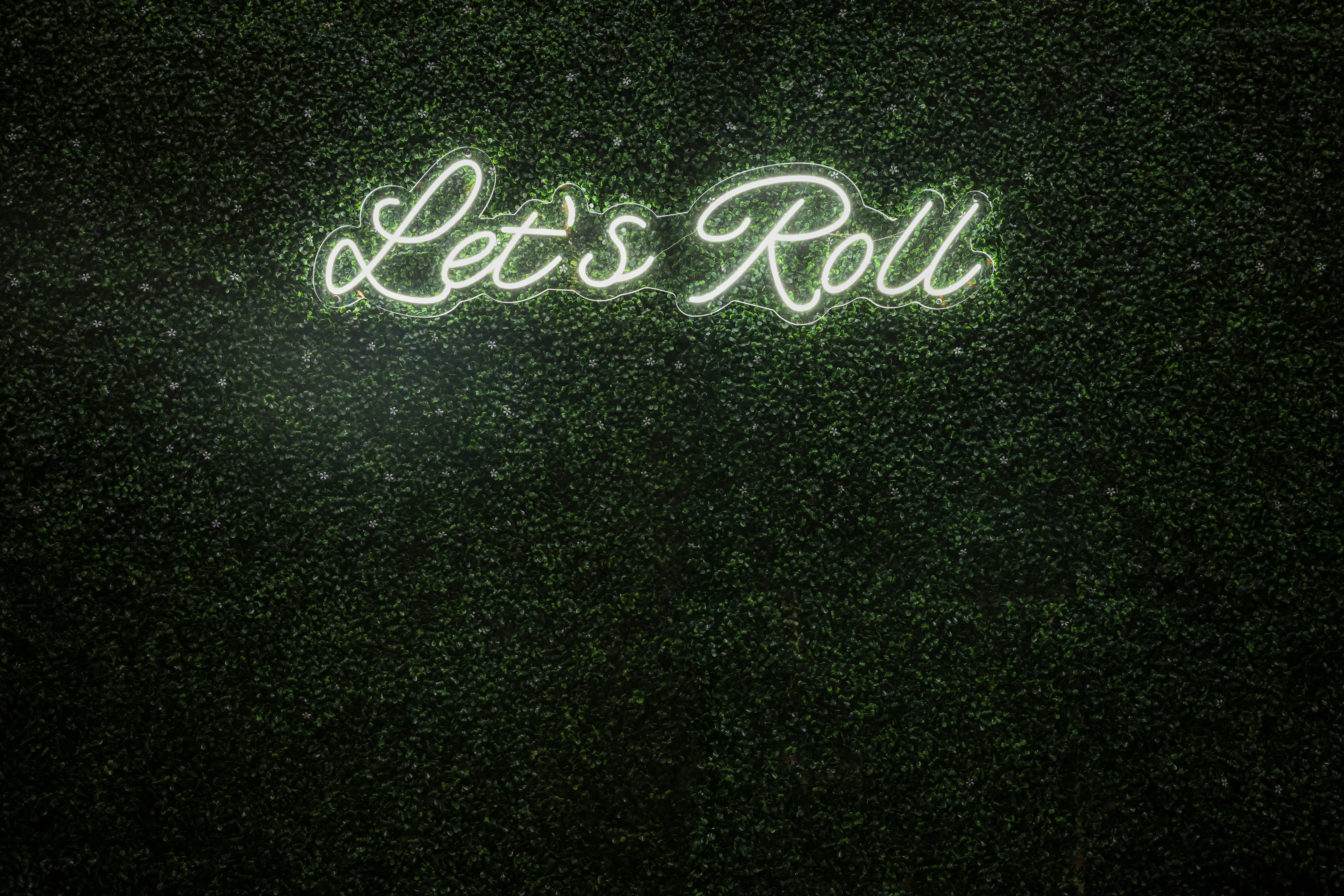 Neon sign reading 'Let's Roll' glows against a textured green wall.