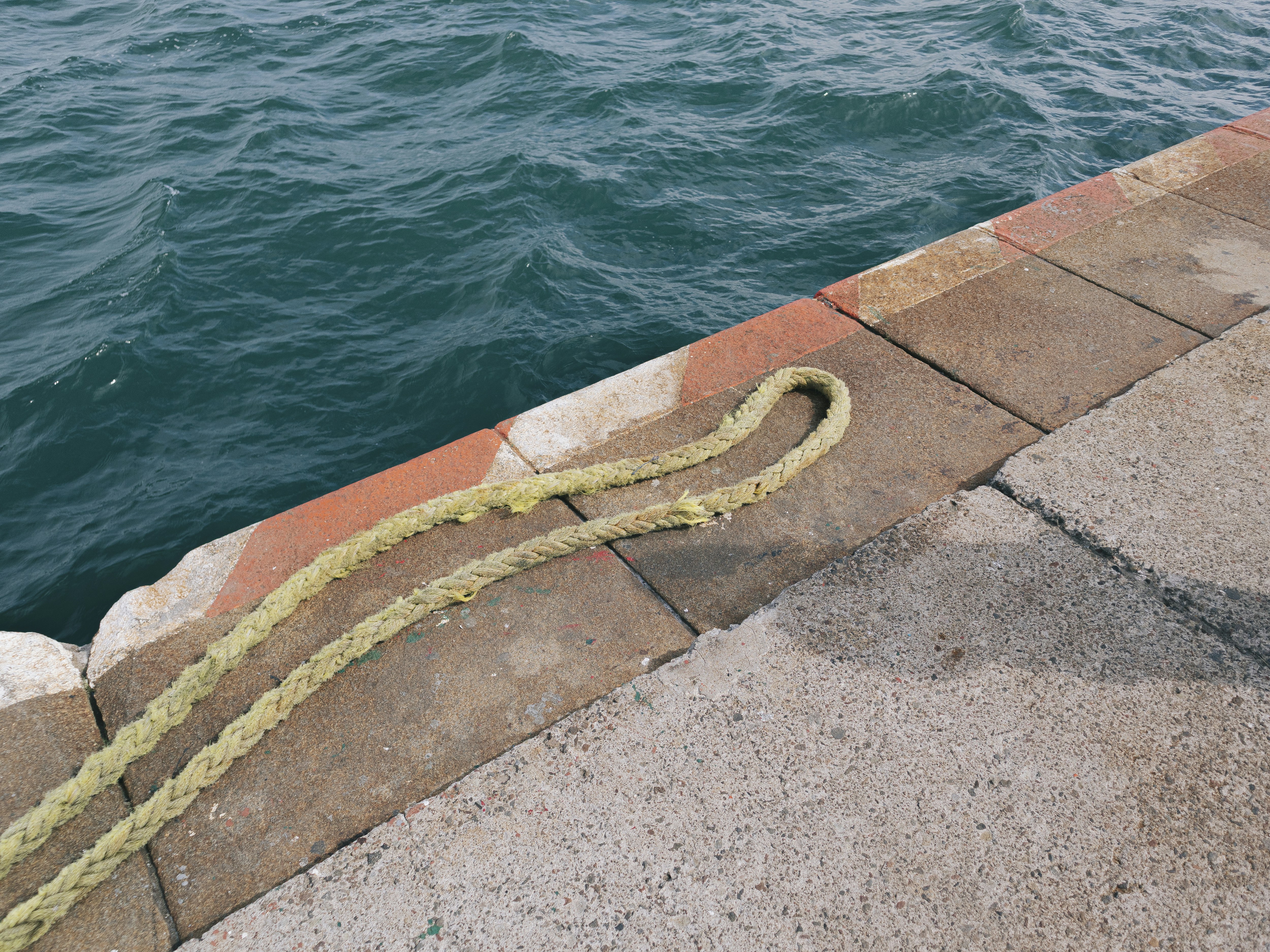 Rope coiled on a sunlit dock beside gently rippling blue water.