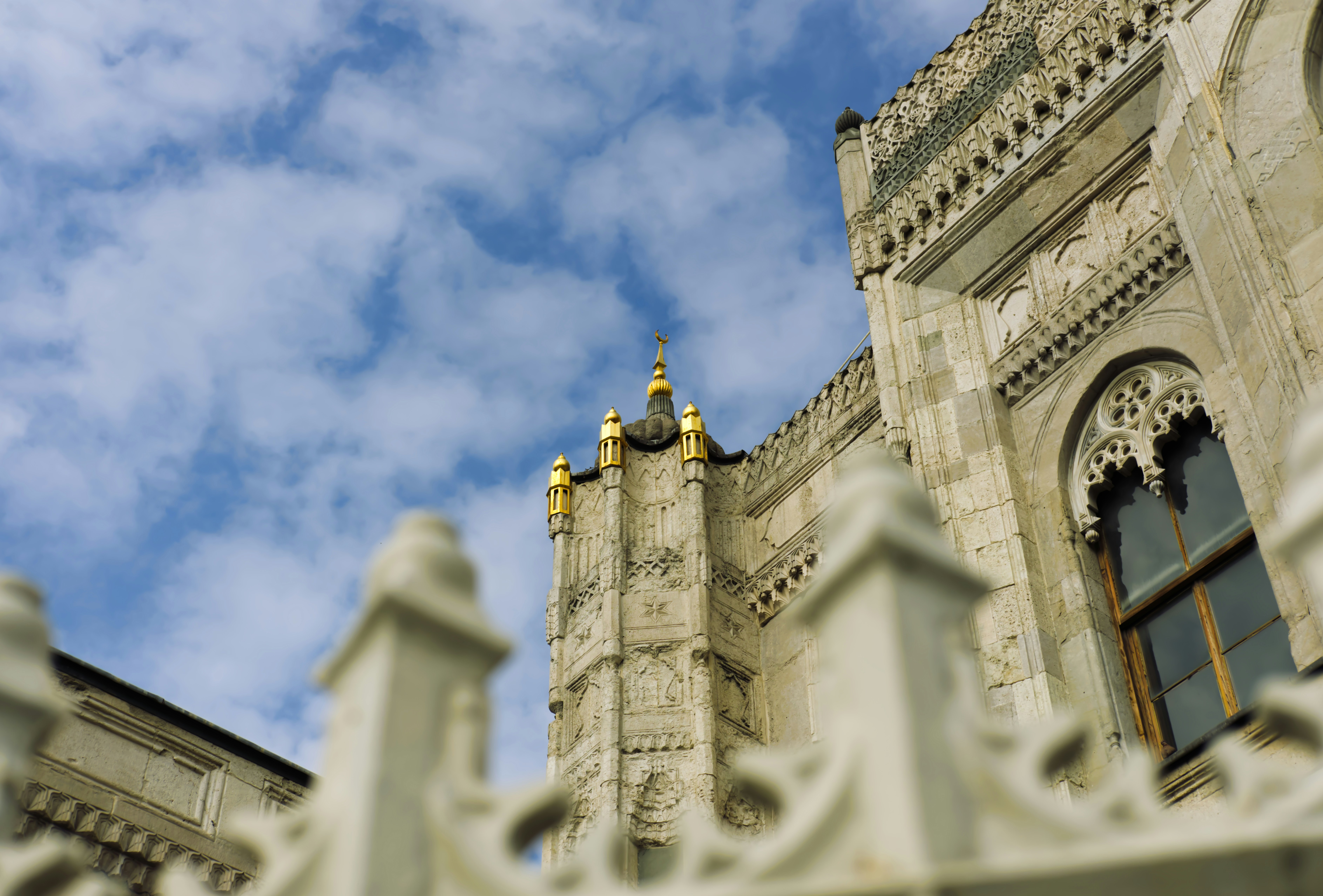 Ornate stone architecture with golden spires framed against a backdrop of blue sky and clouds.