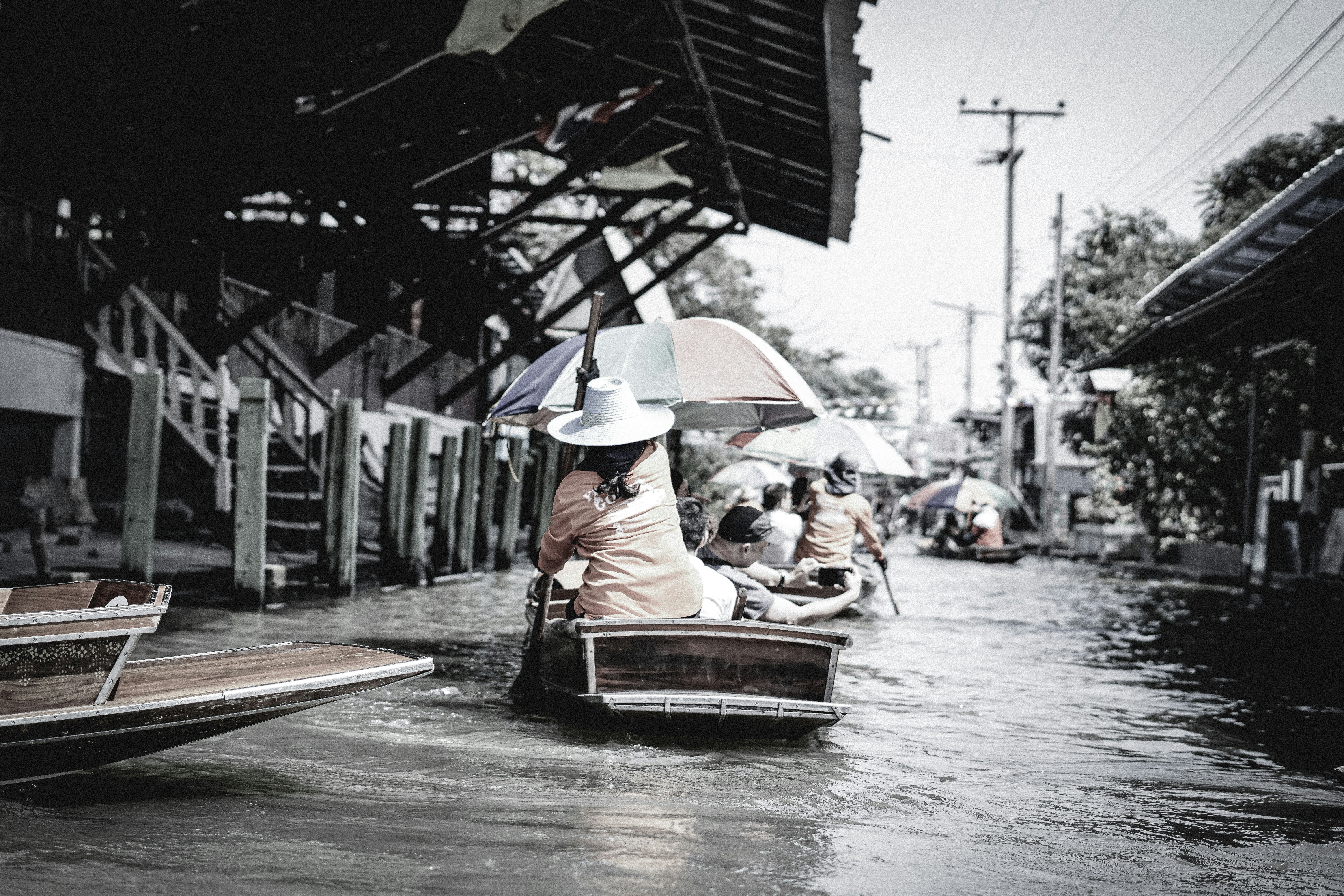 Boats navigate a bustling canal with vendors and tourists under colorful umbrellas.
