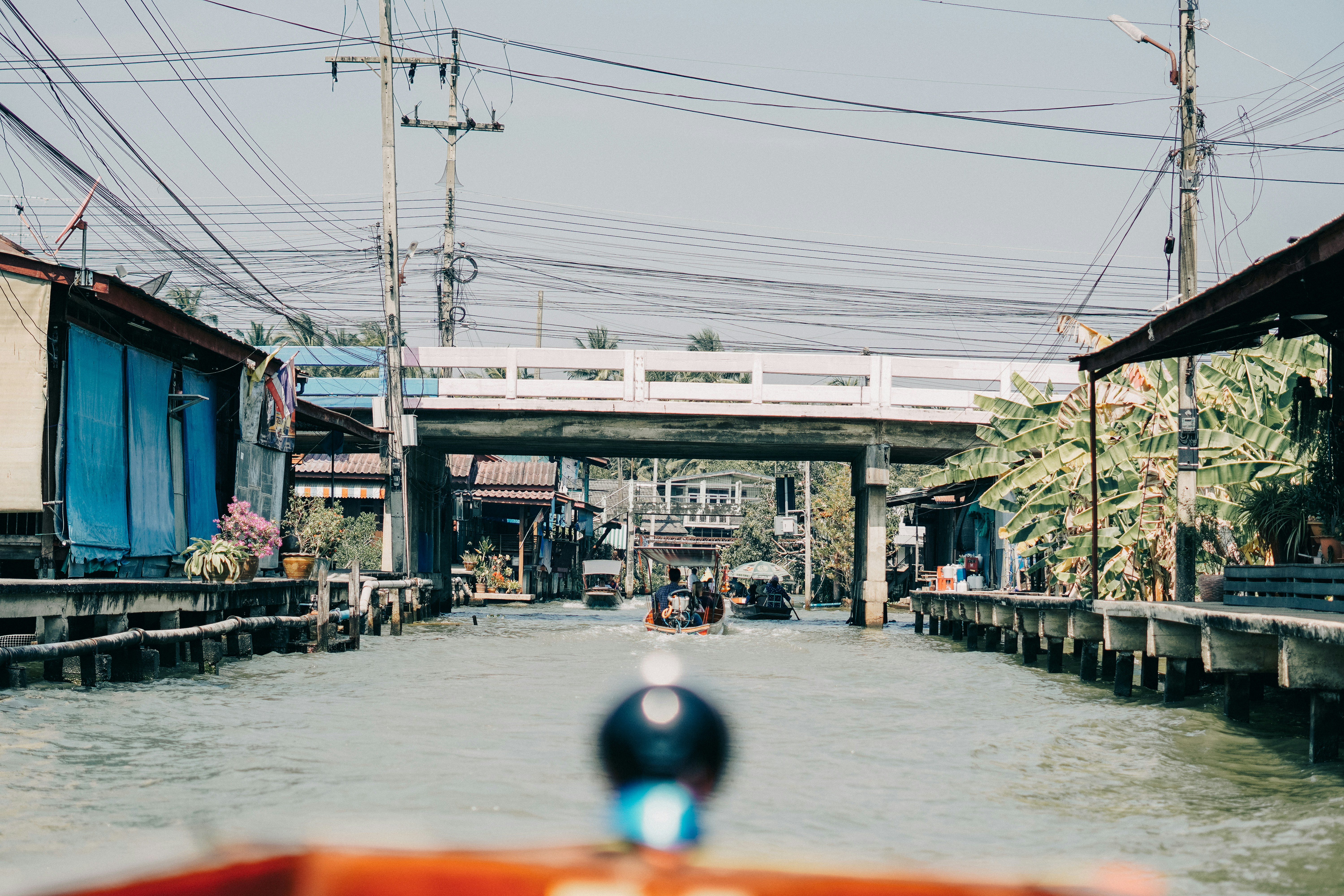 Narrow canal with vibrant houses and boats under a concrete bridge.