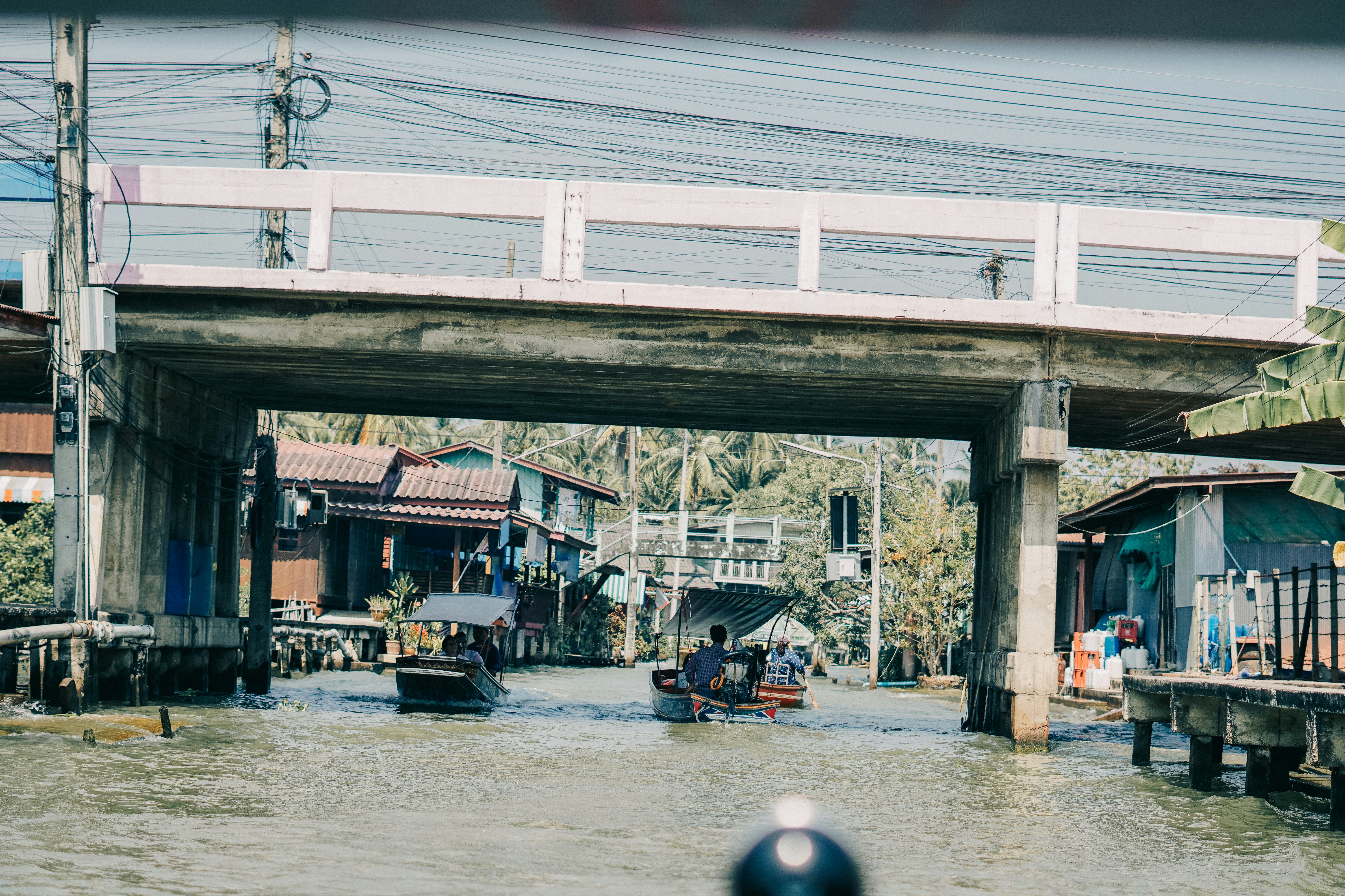Boats navigating a narrow canal beneath a concrete bridge surrounded by colorful houses.