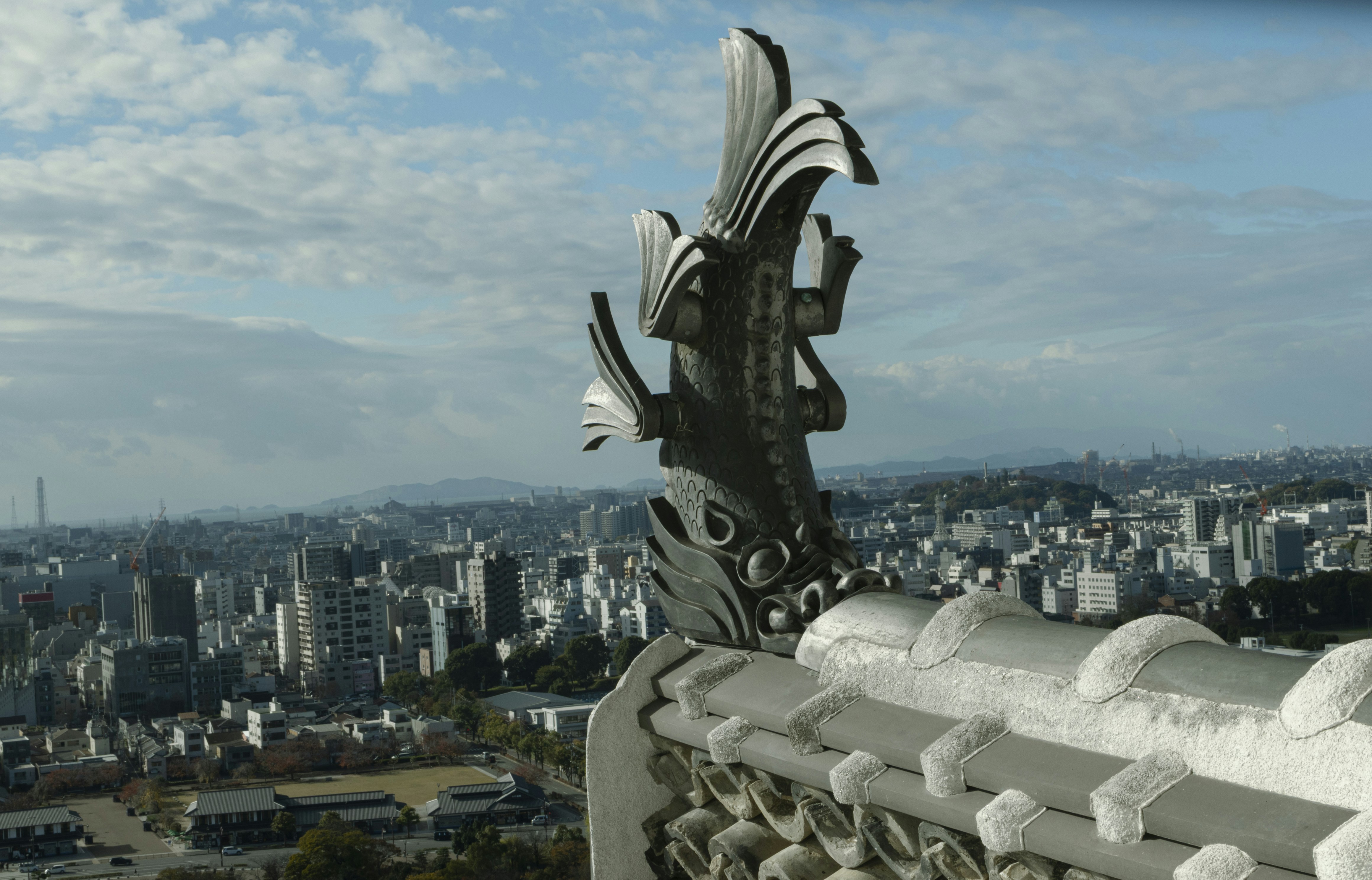 Ornate shachihoko statue perched atop Himeji Castle with urban landscape in the background.