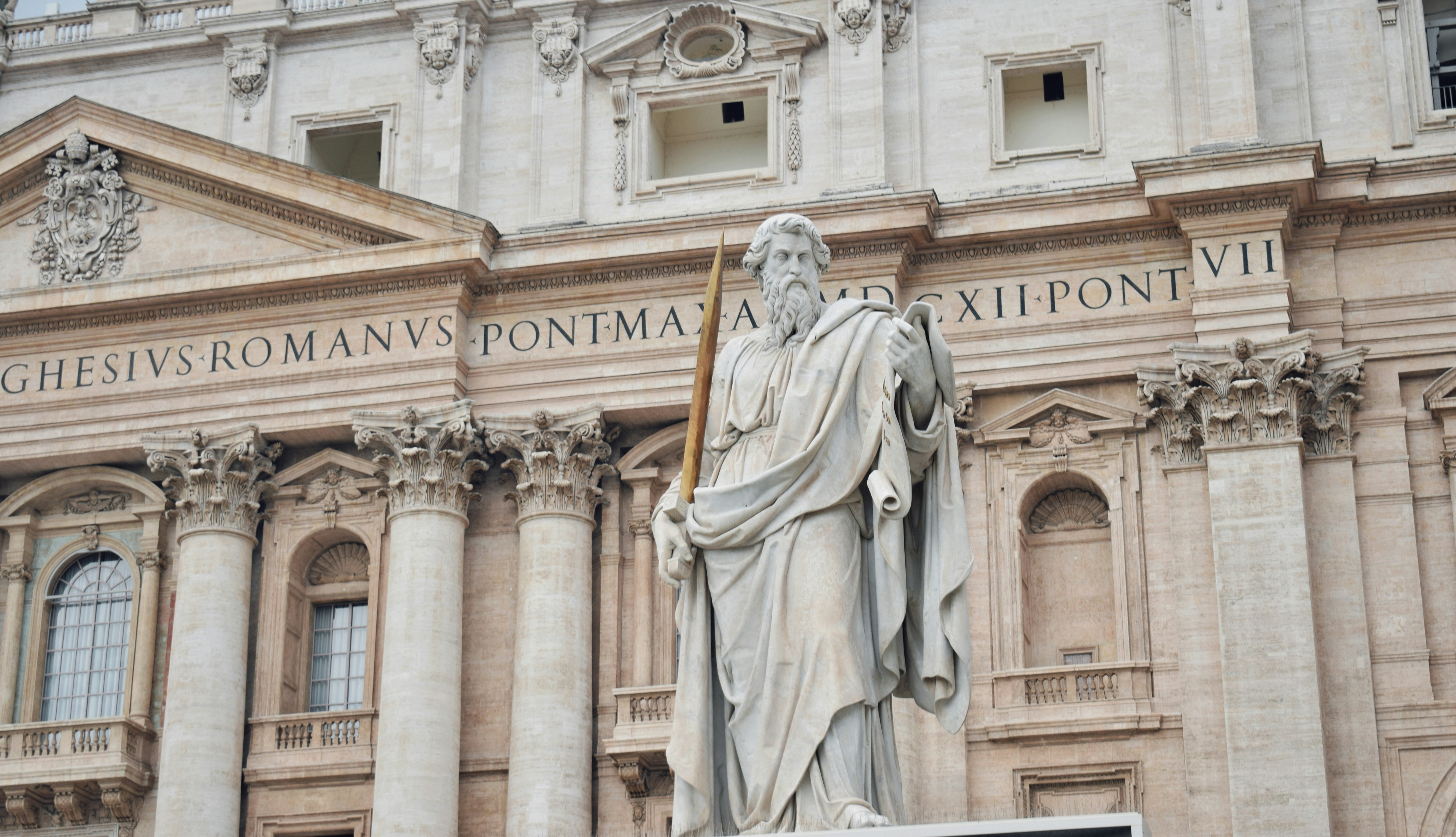 Marble statue holding a sword stands before ornate architectural facade of St. Peter's Basilica.