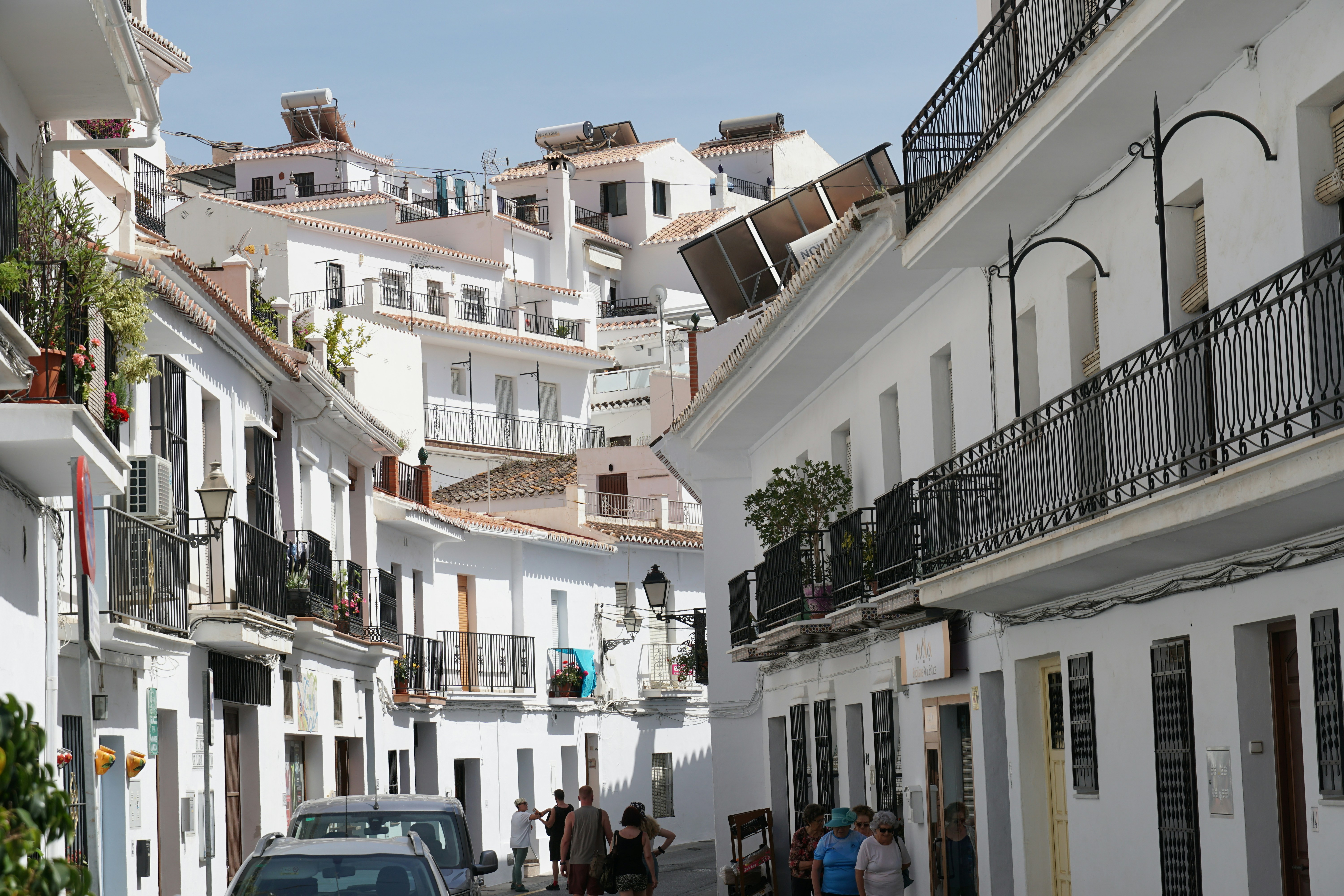 Whitewashed buildings with terracotta roofs line a narrow street under a clear blue sky.