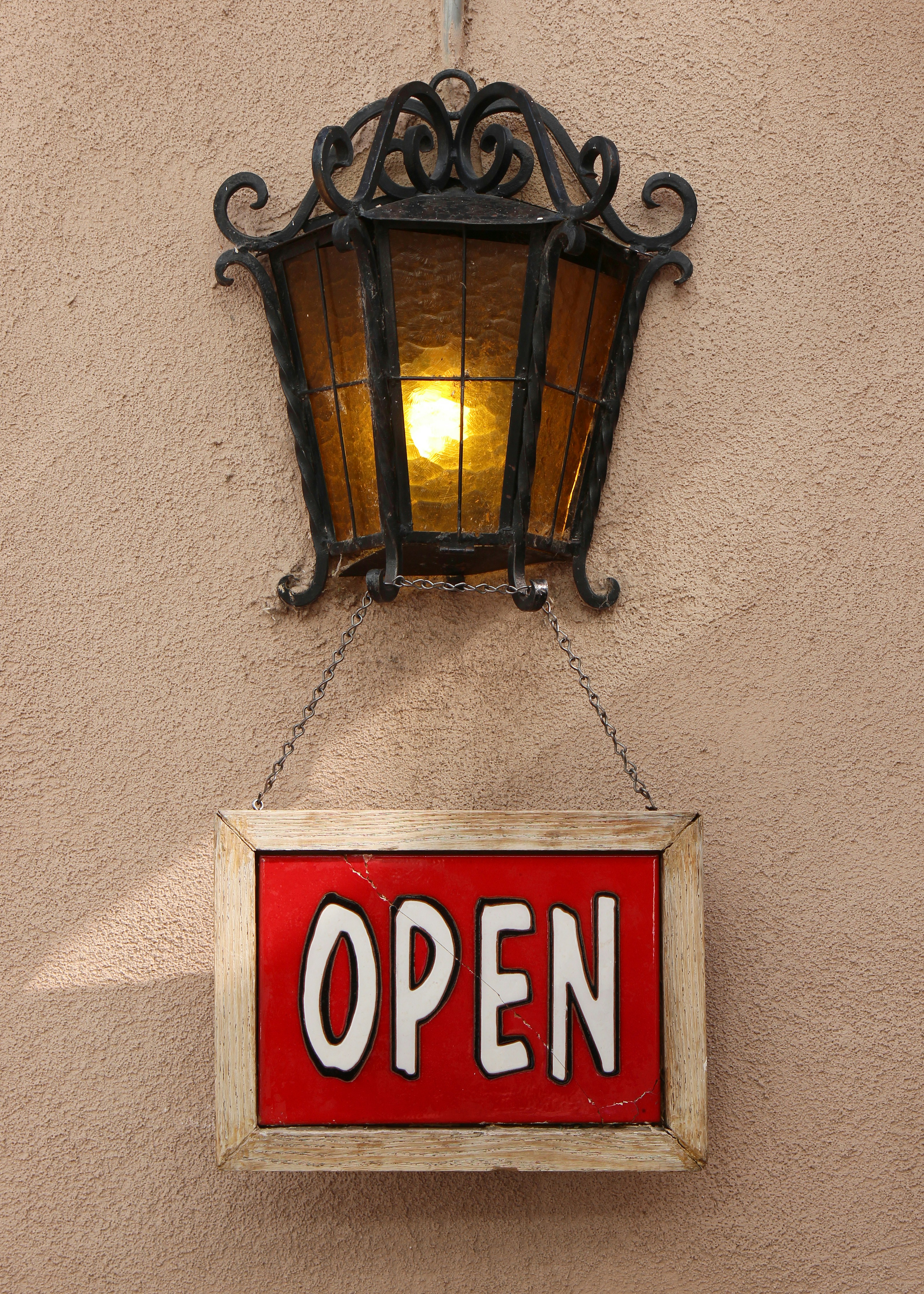 Lantern Glow Over a Hanging Open Sign on a Sun-Warmed Stucco Wall