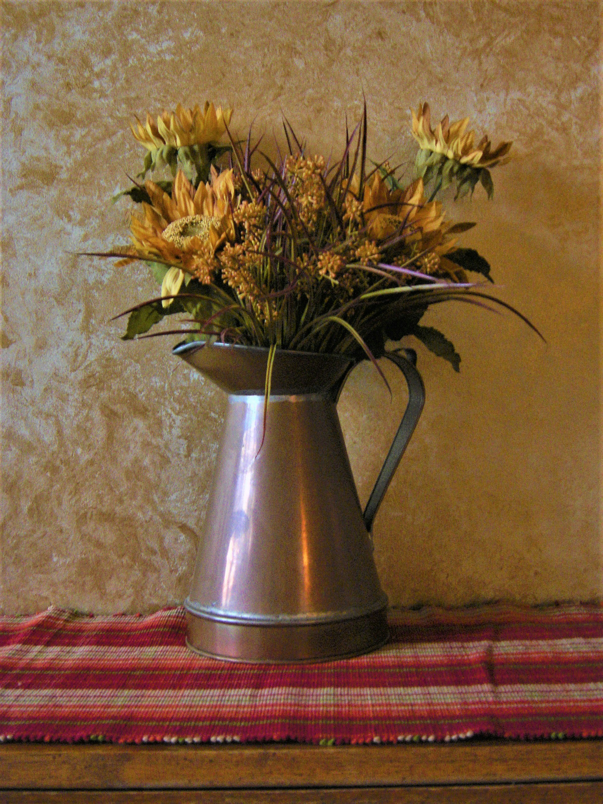 Flowers in a copper pitcher on a table.