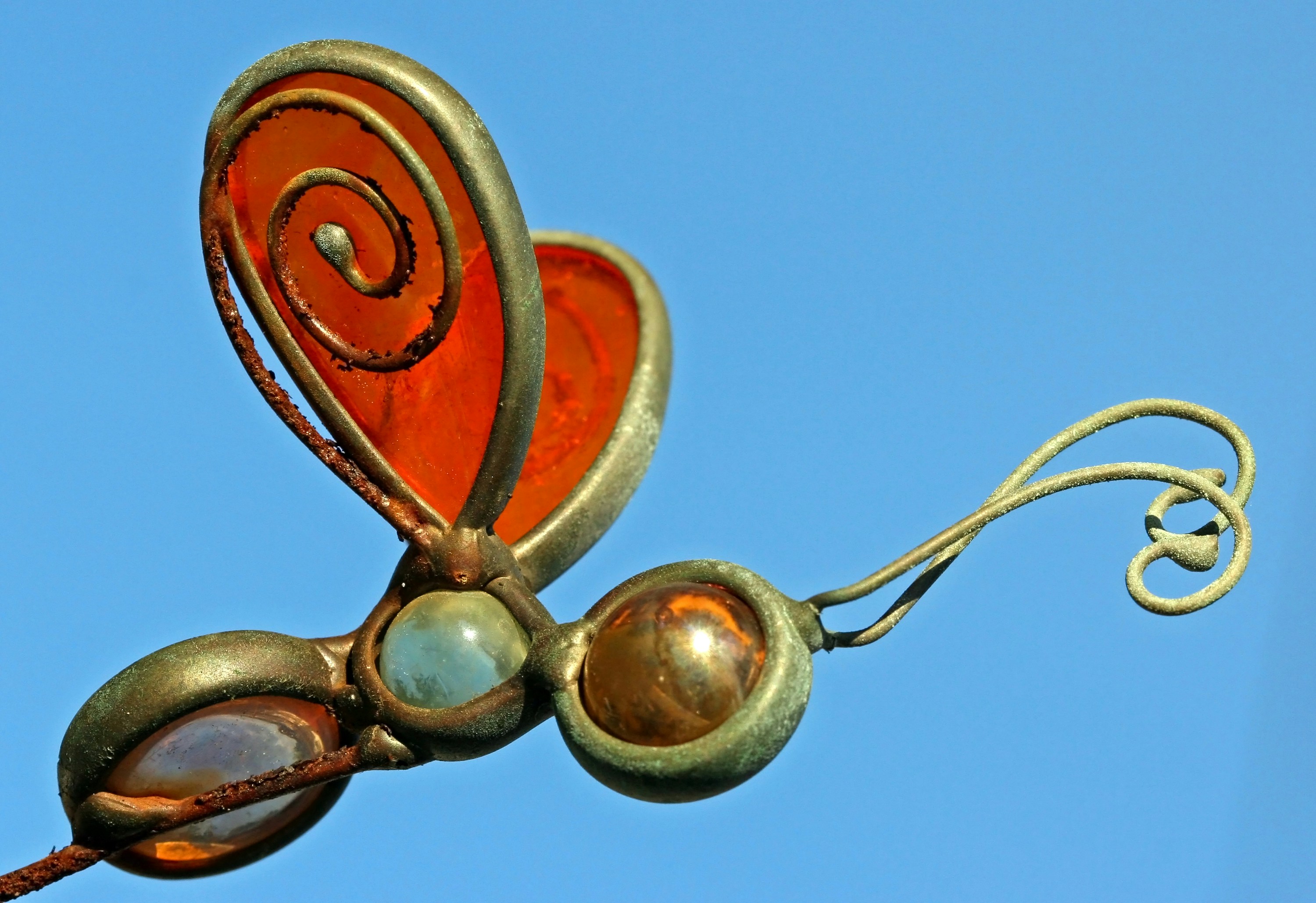 Metal and glass butterfly sculpture with vibrant wings against a clear blue sky.