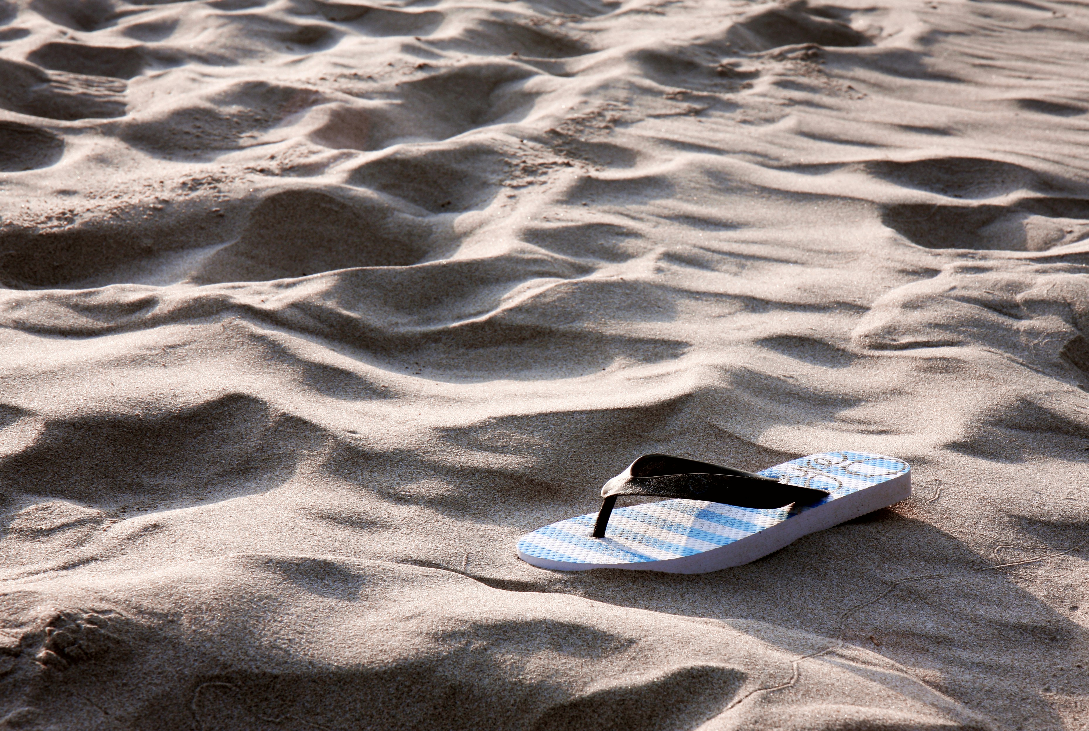 Blue checkered flip-flop resting on rippled sandy beach in afternoon light.