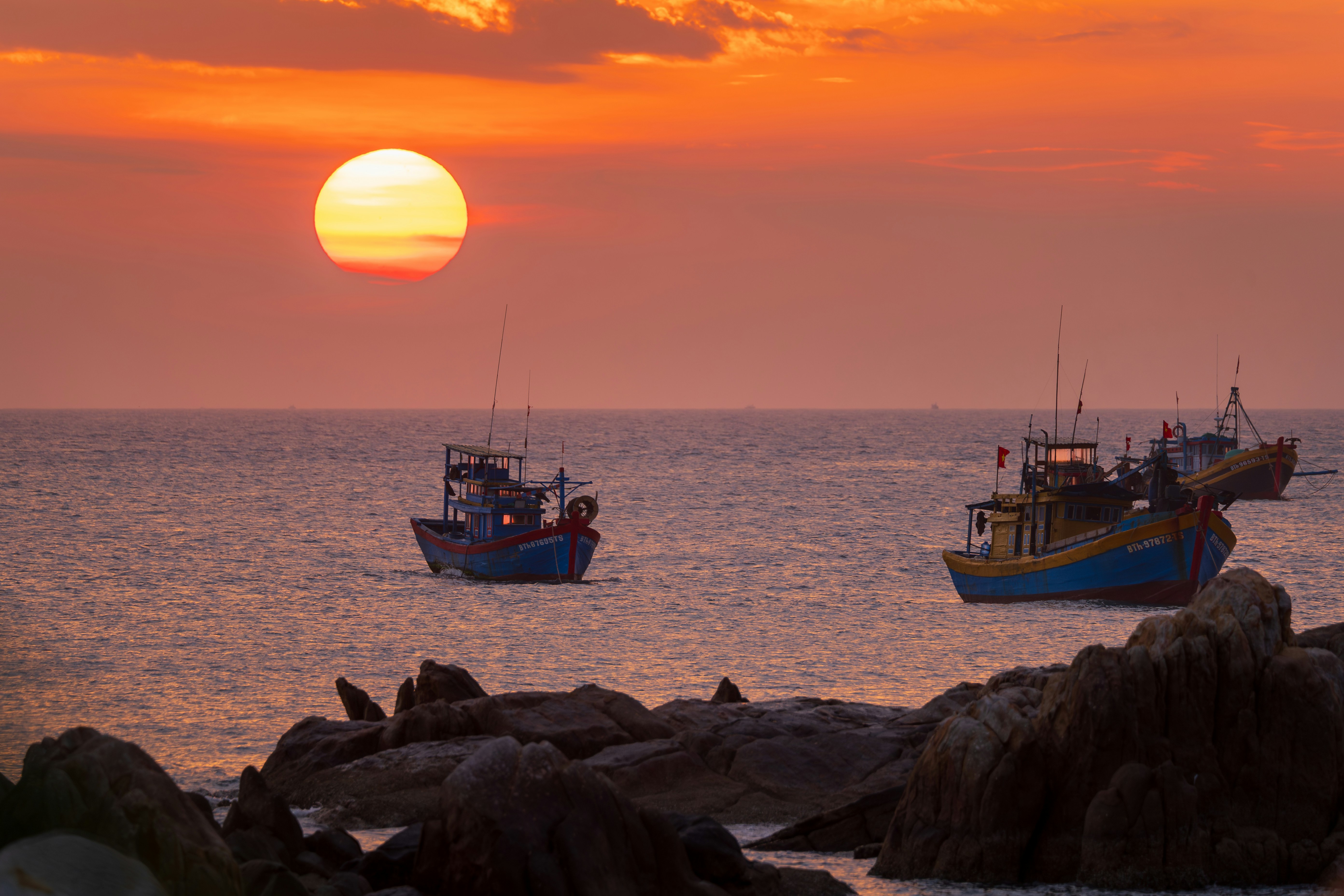 Fishing boats rest in a tranquil bay under a vibrant orange sunrise.