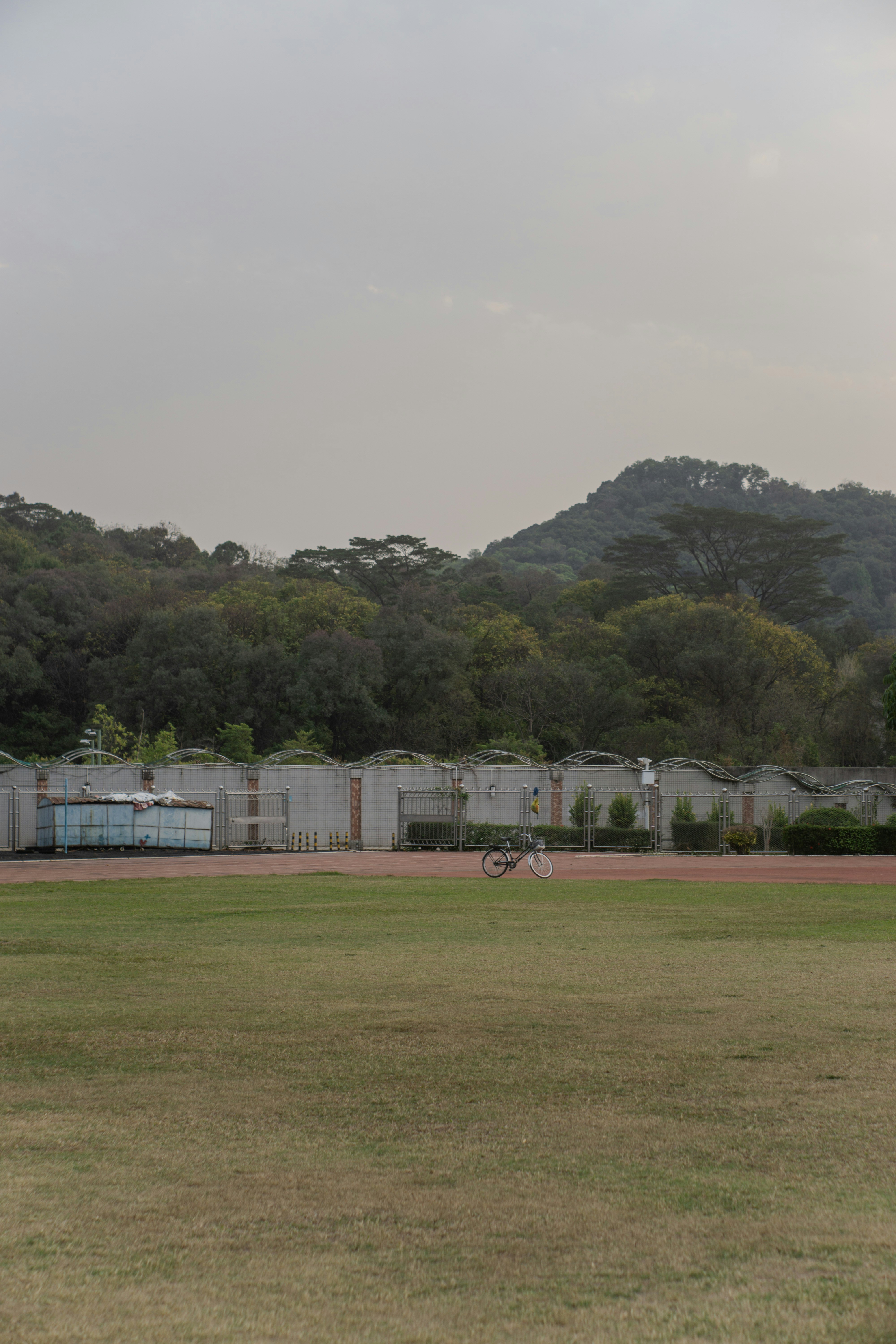 A lone bicycle rests on an empty athletic track, framed by lush greenery and distant hills. The scene evokes a sense of tranquility and reflection.