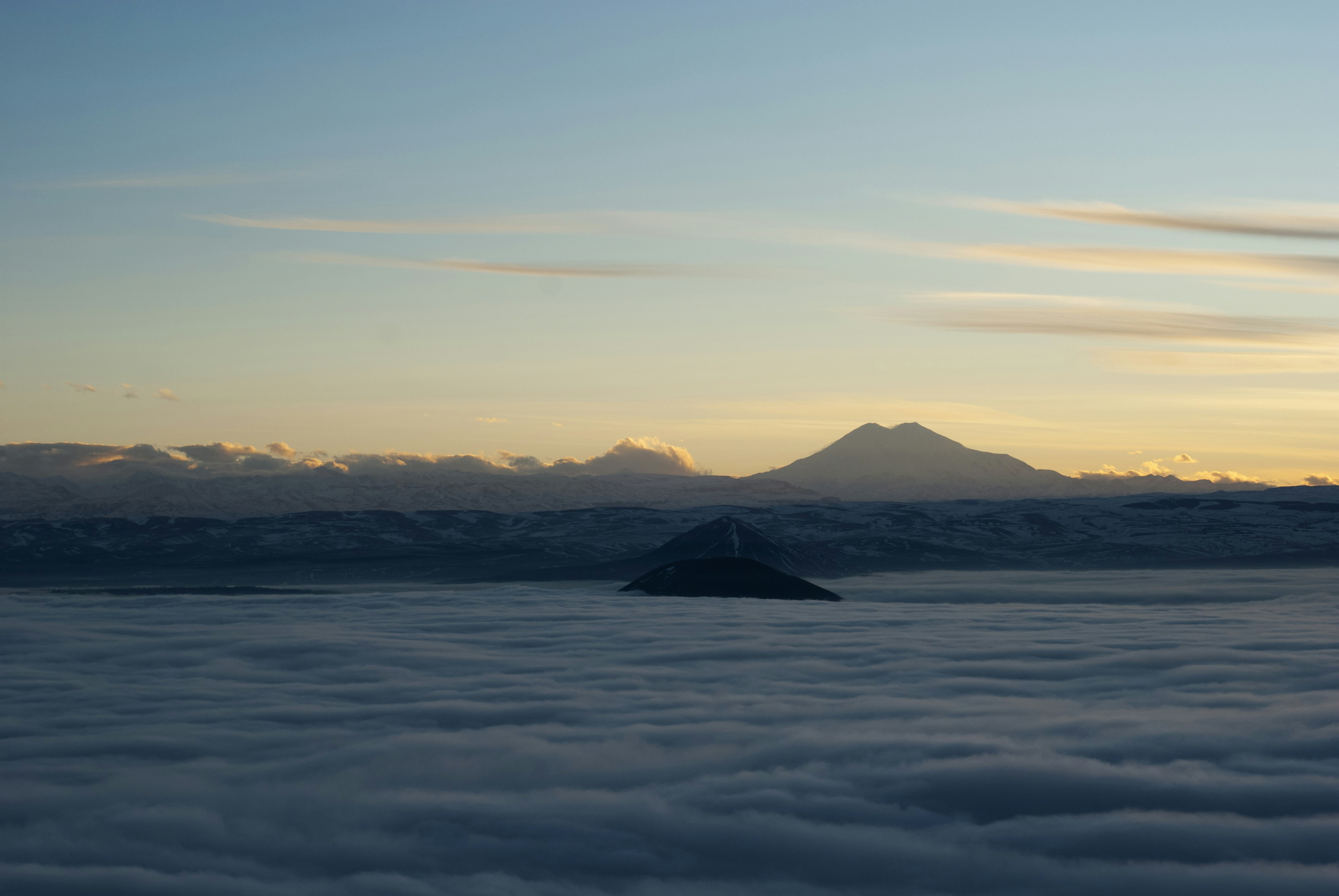 Golden sunset over distant mountains with a blanket of clouds below.