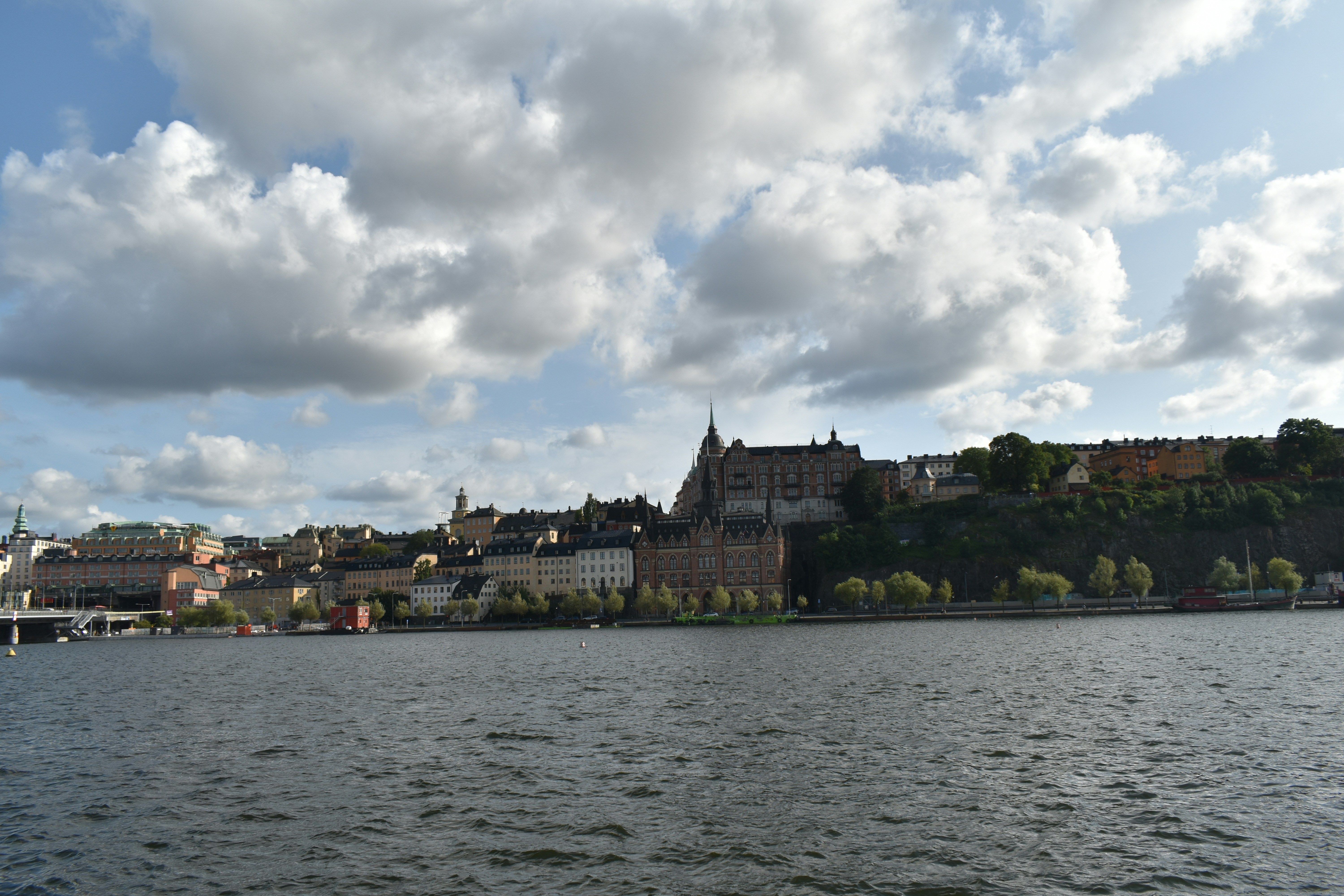 Historic buildings line the Stockholm waterfront under a sky dotted with clouds.