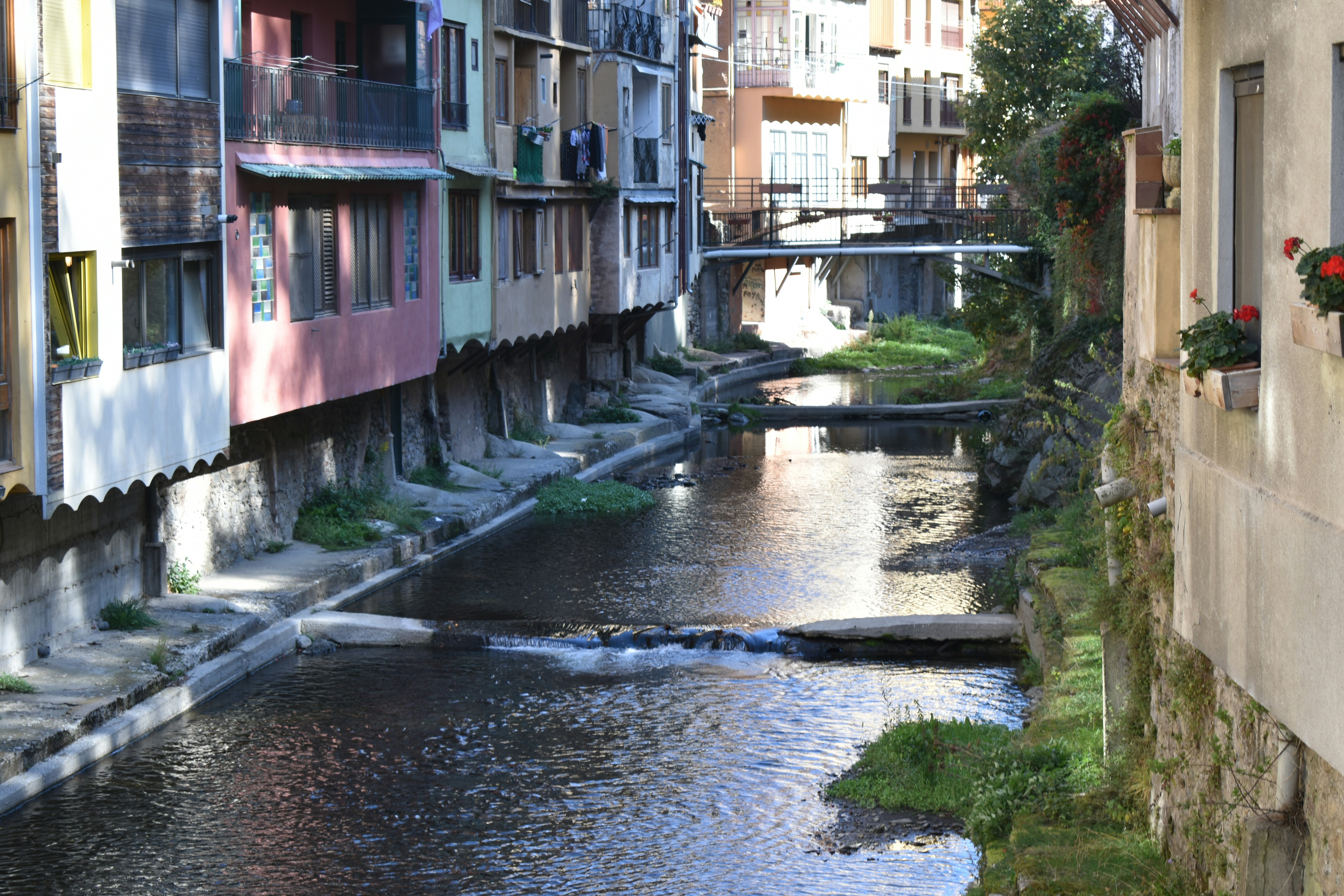 Vibrant buildings line a narrow river, with sunlight creating reflections on the water.