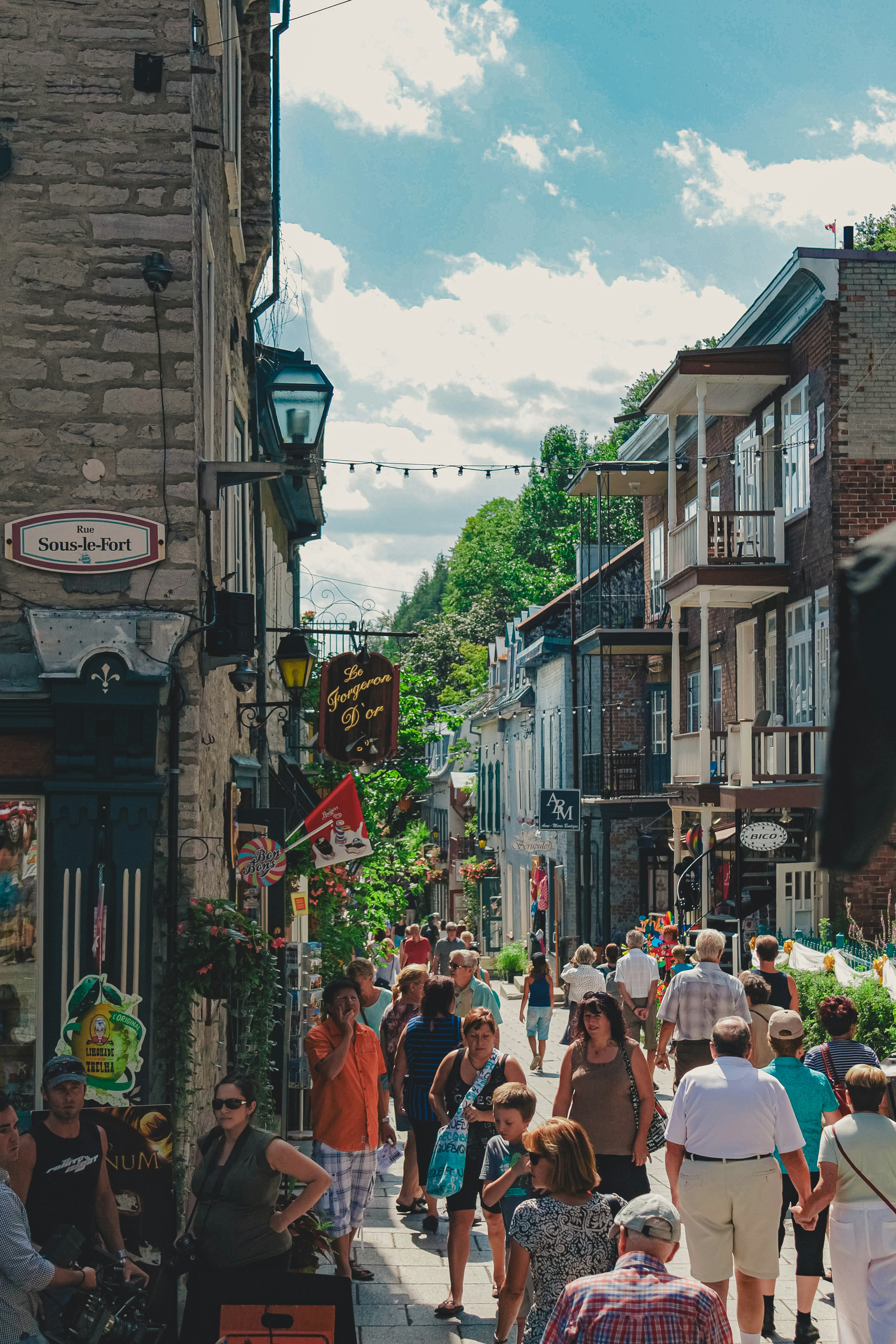 Crowded pedestrian street lined with historic buildings under a bright blue sky.