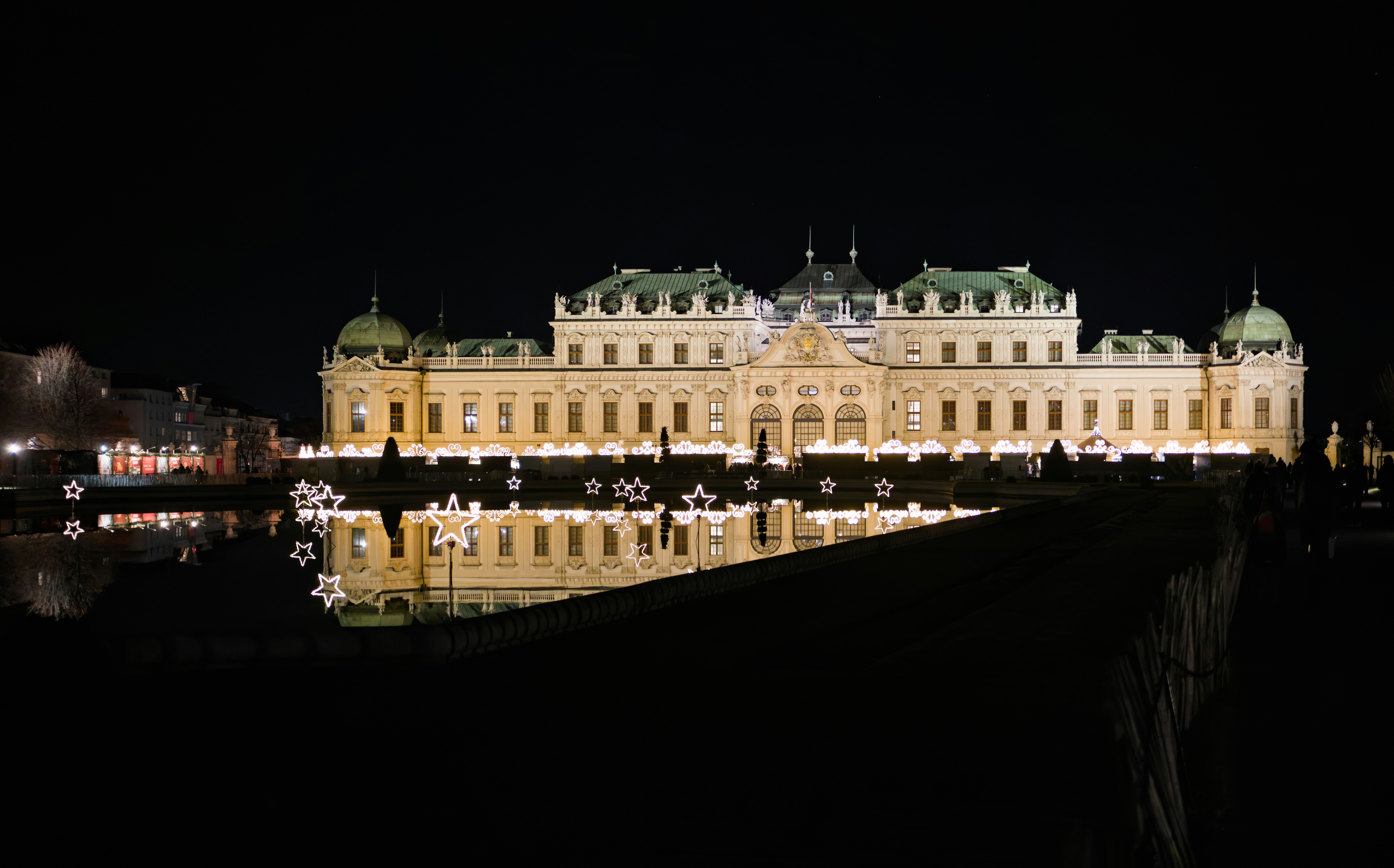 Belvedere Palace illuminated against the night sky, reflecting in the tranquil water adorned with star-shaped lights.