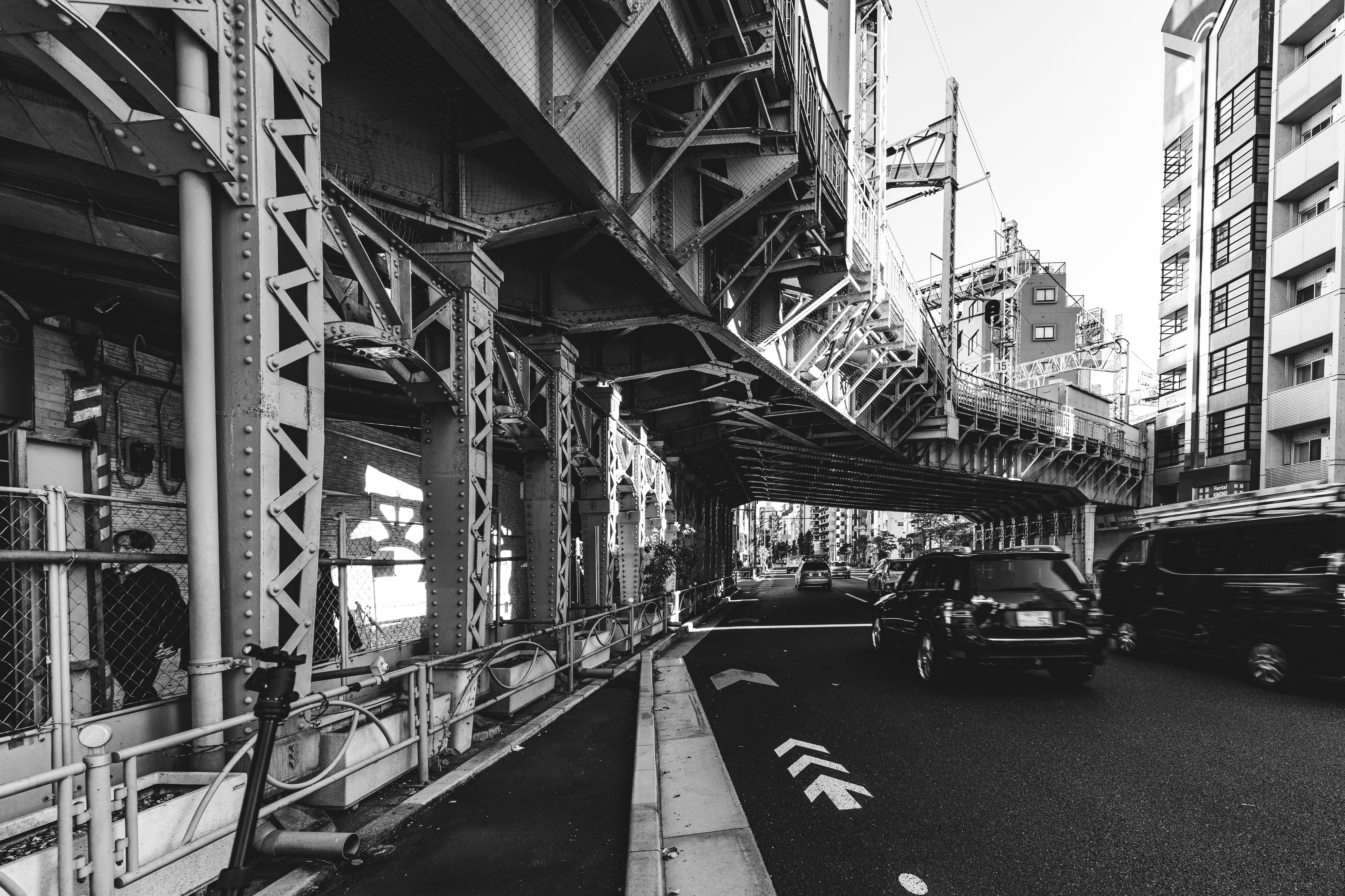 Monochrome cityscape of cars driving under an intricate steel bridge.