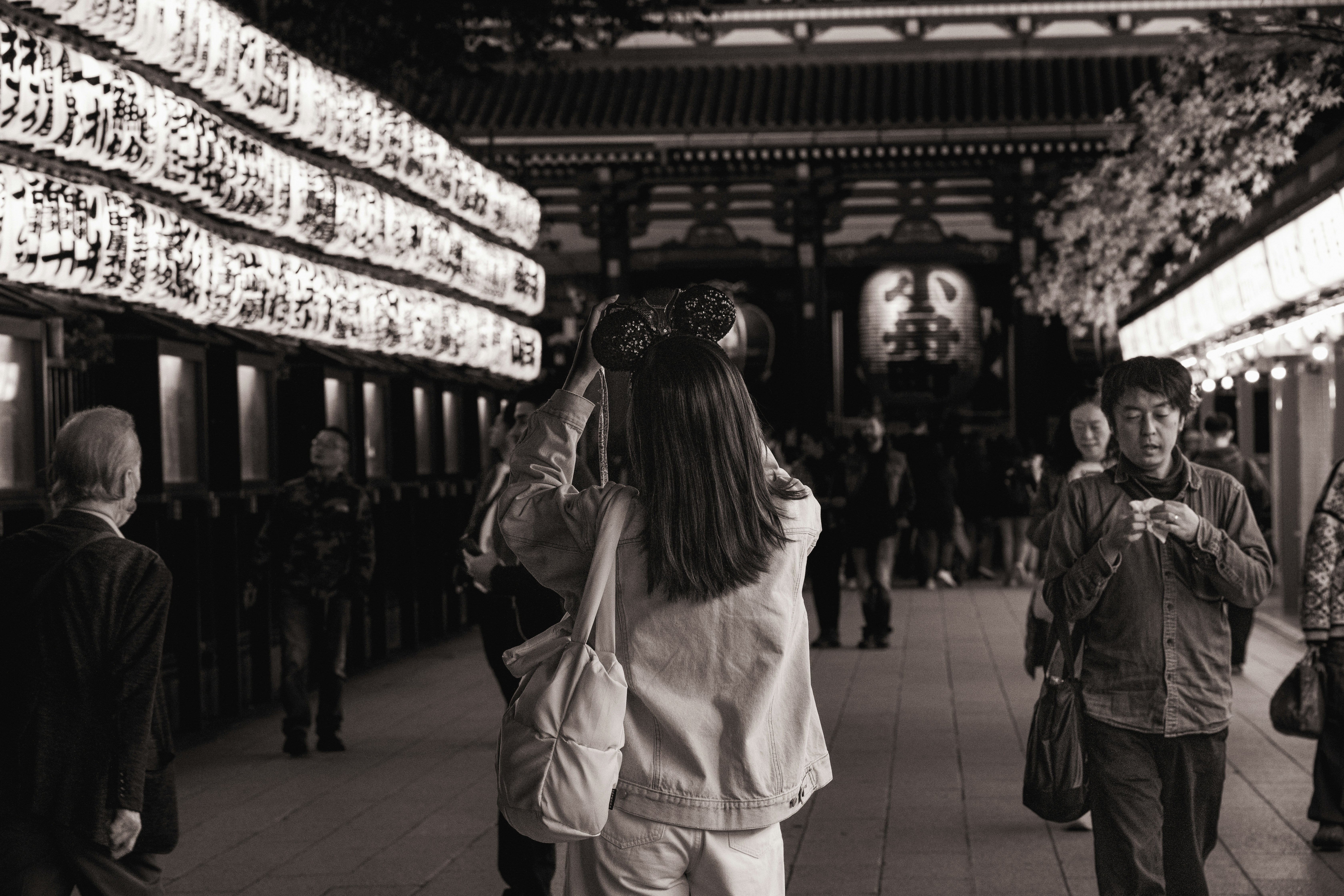 Person with mouse ears in a crowd under illuminated lanterns at night.
